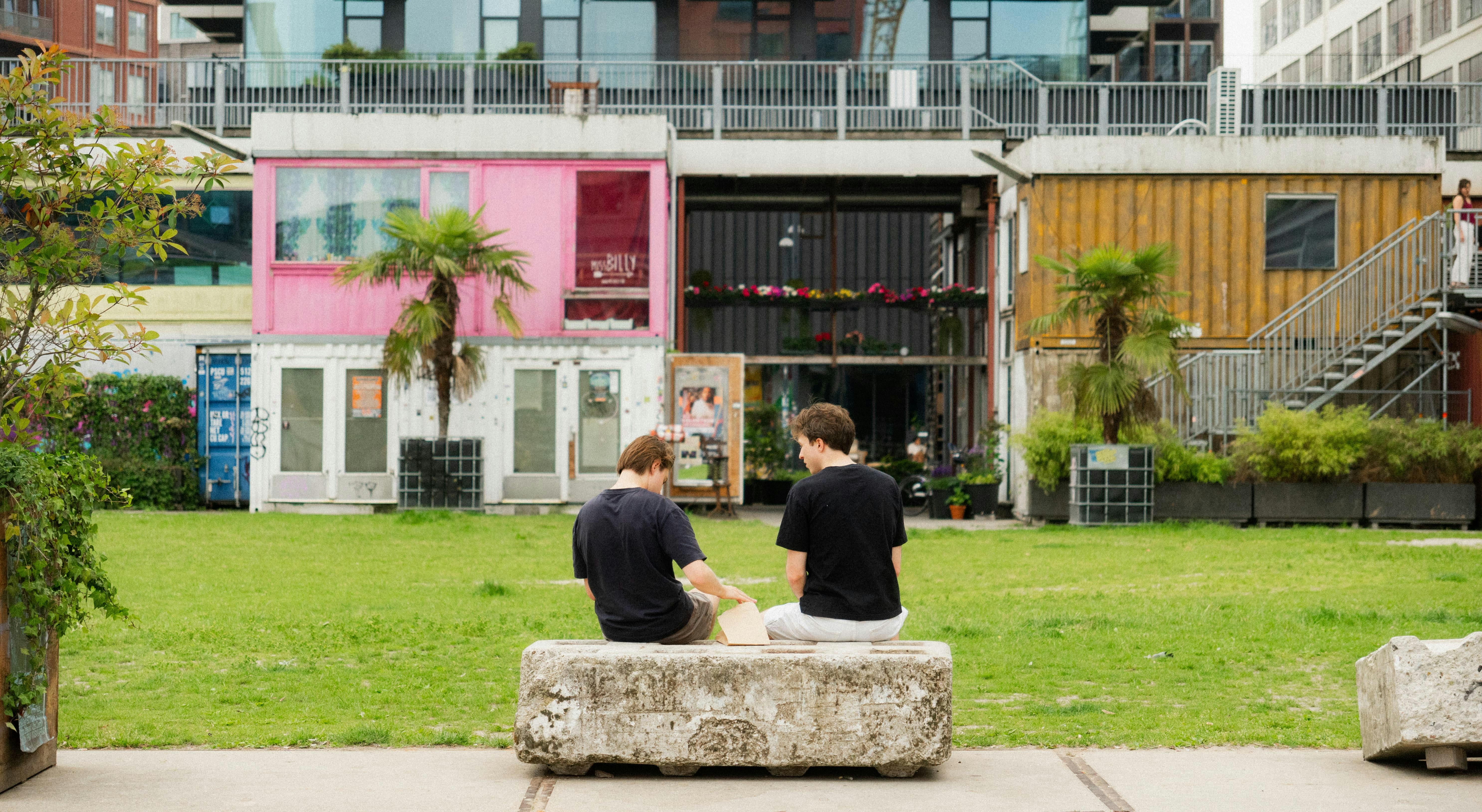 Two Friends on a Concrete Bench Overlooking a Colorful Courtyard