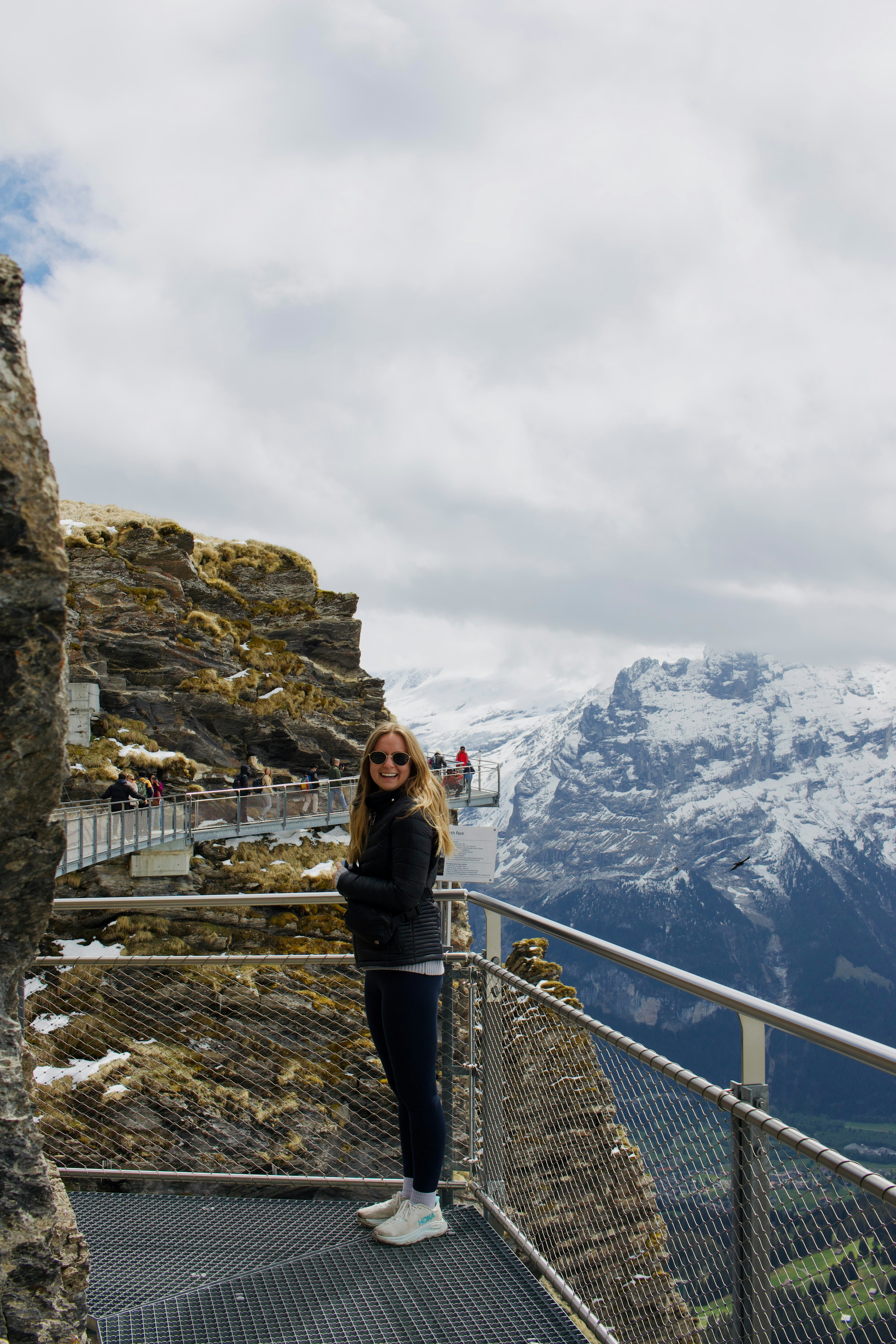 Cliffside watcher: a woman steadies on a scenic overlook above snowy peaks