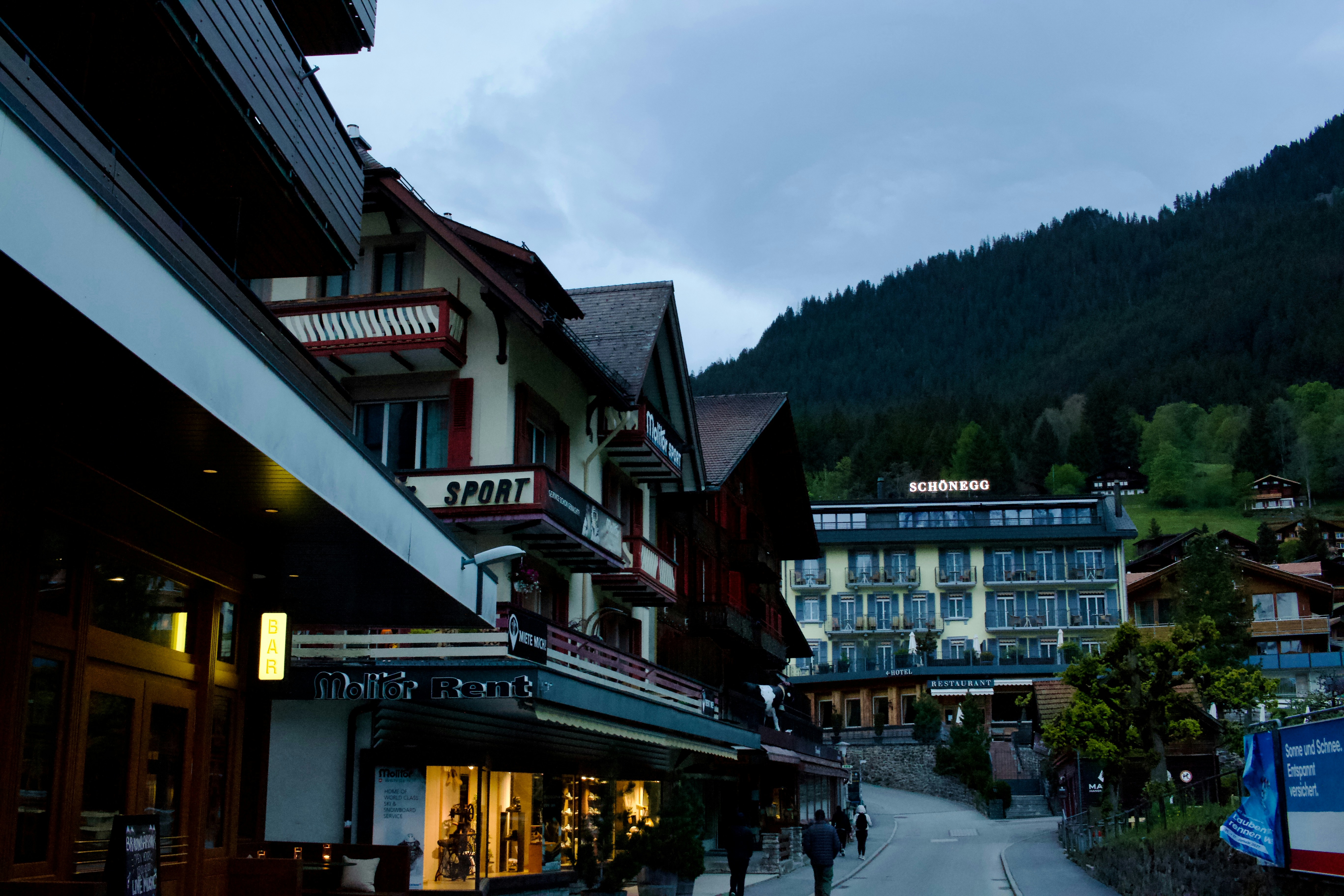 Alpine Village at Dusk: Shopfronts and Windows Glow Beneath a Mountain Road