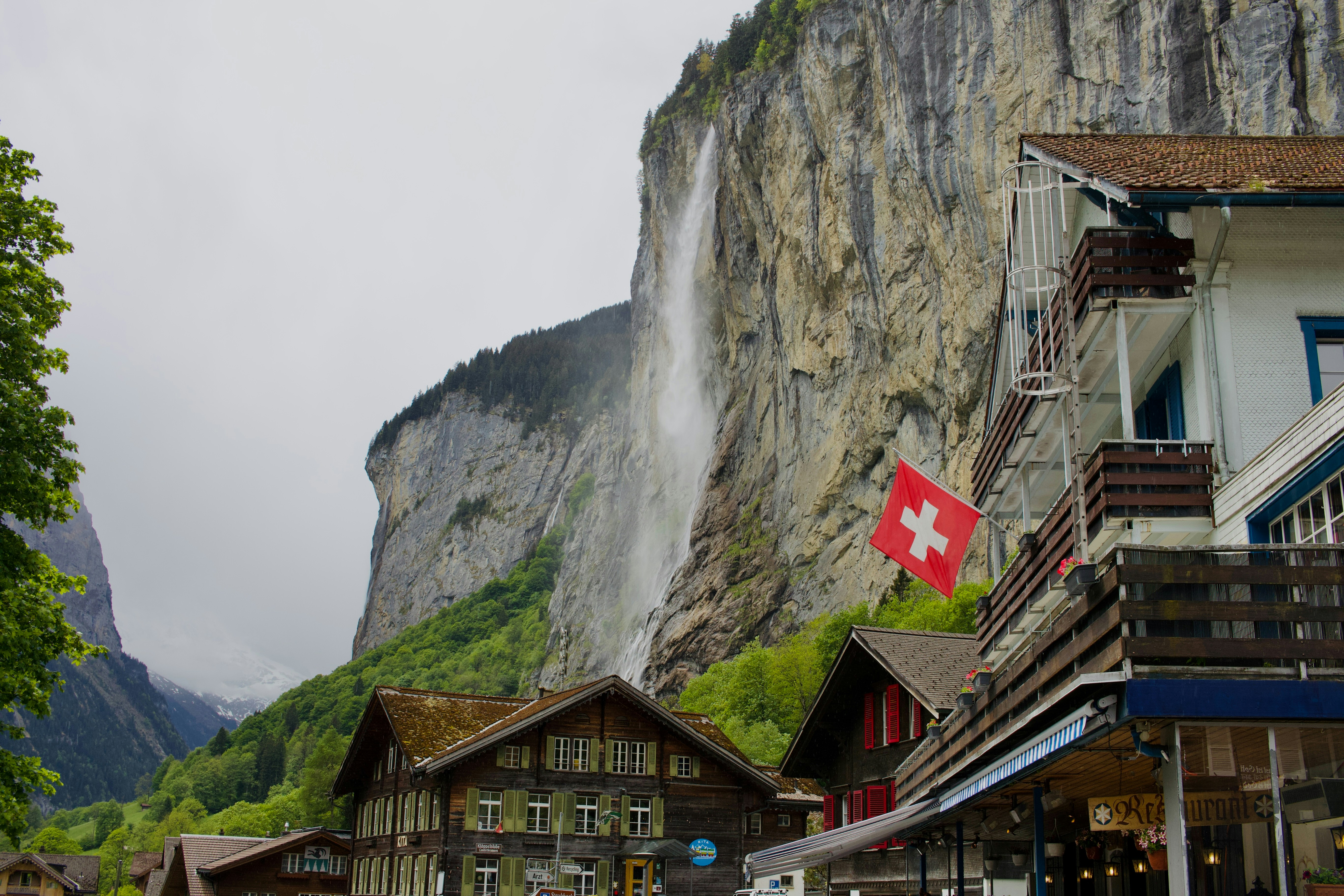Swiss Village by the Waterfall: Alps, Timber Facades, and a Flag by the Red Roof