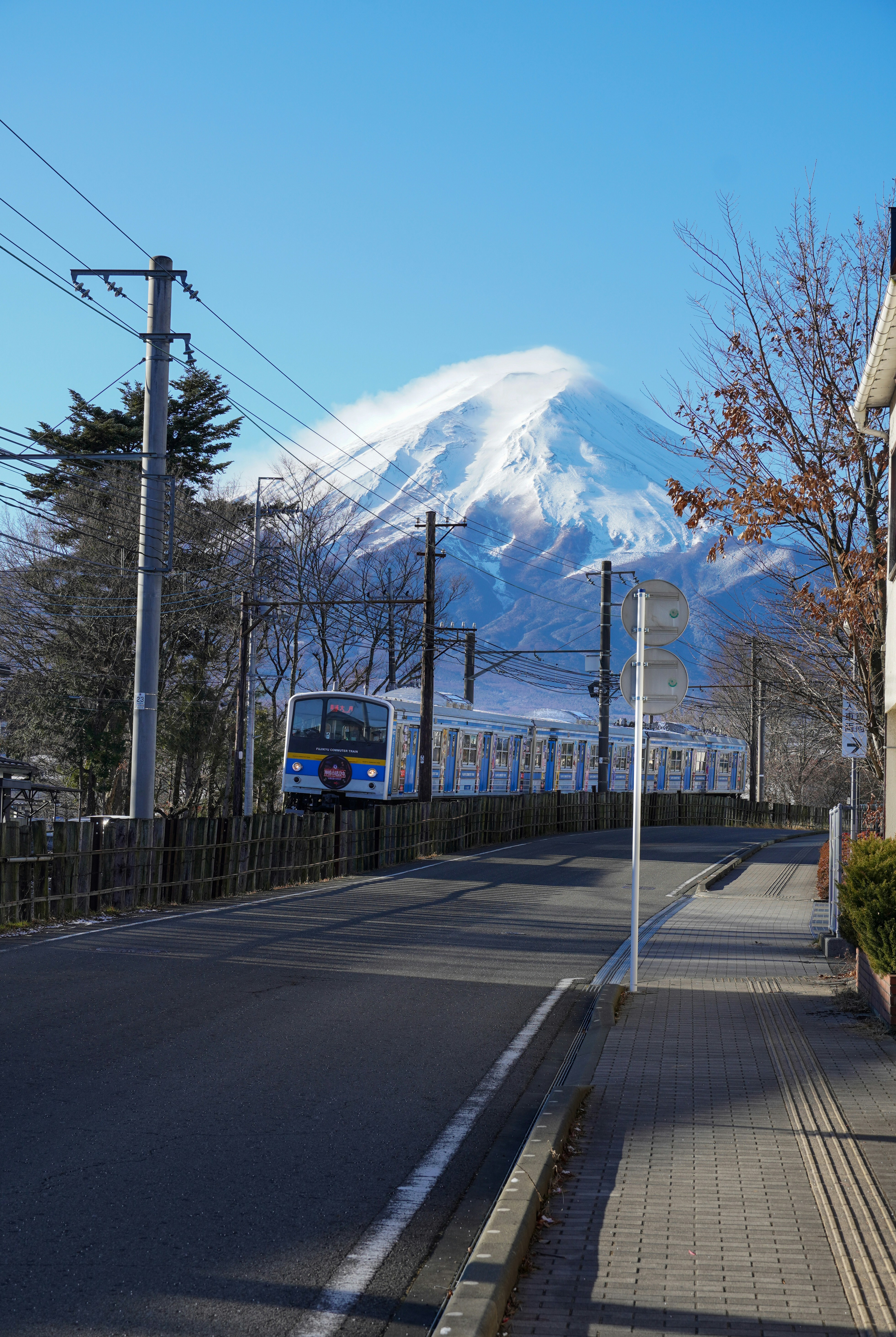 Blue train passes snow-capped mount fuji under clear sky.
