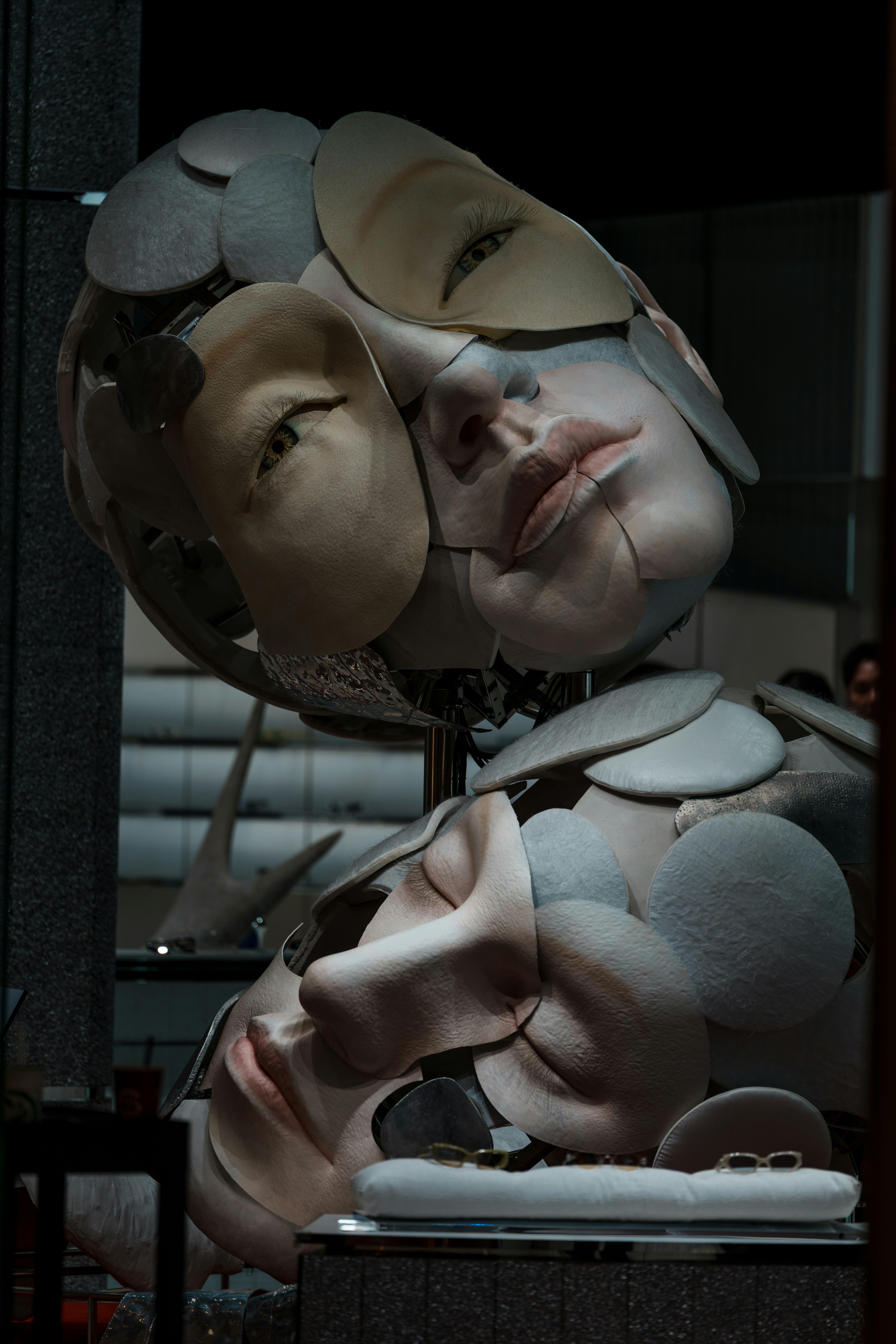 Sculptural faces assembled from soft, overlapping fragments create a surreal portrait in a dim display space. The installation emphasizes tactile textures and a layered, mask-like composition.