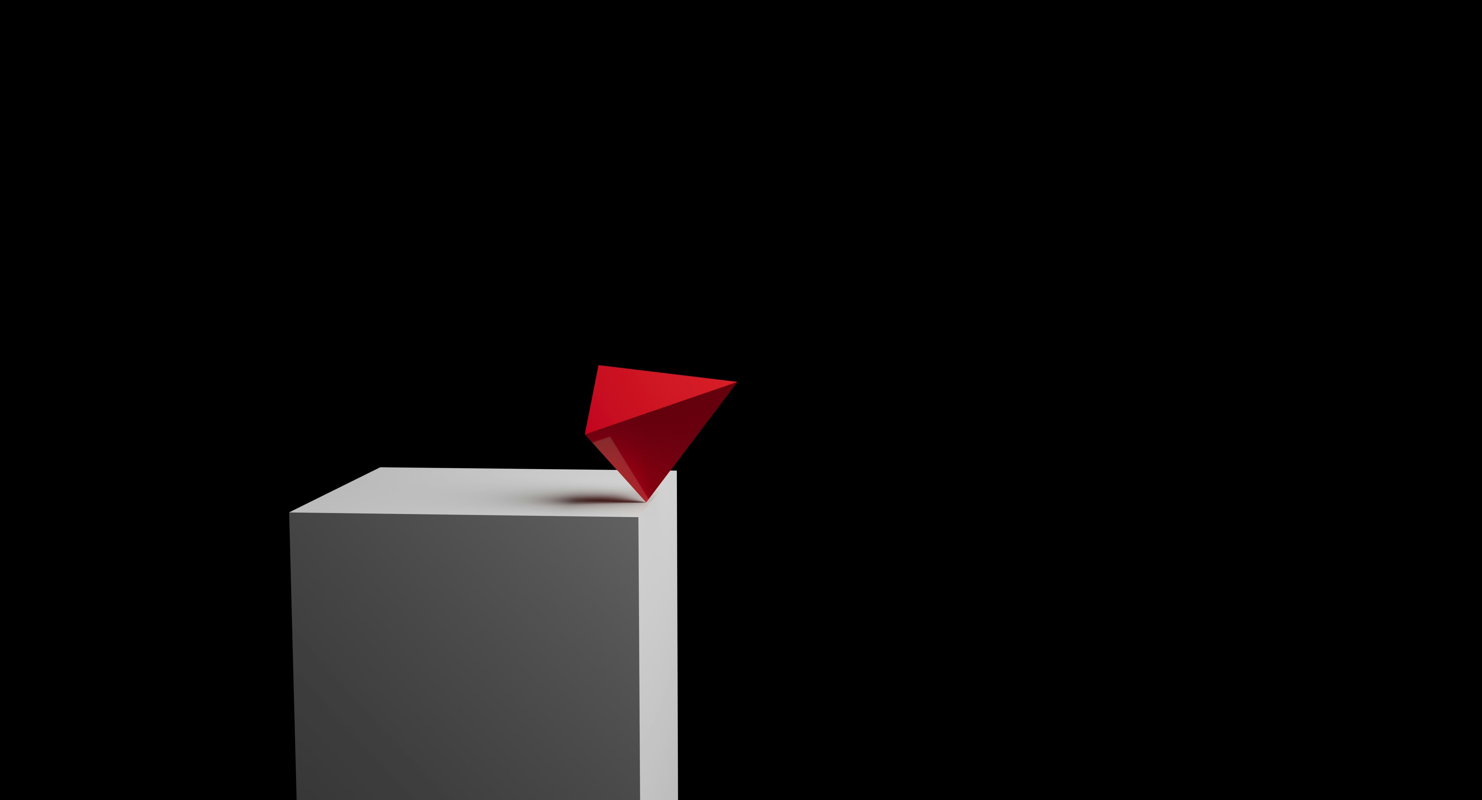 Red polyhedron balancing on the edge of a white block.