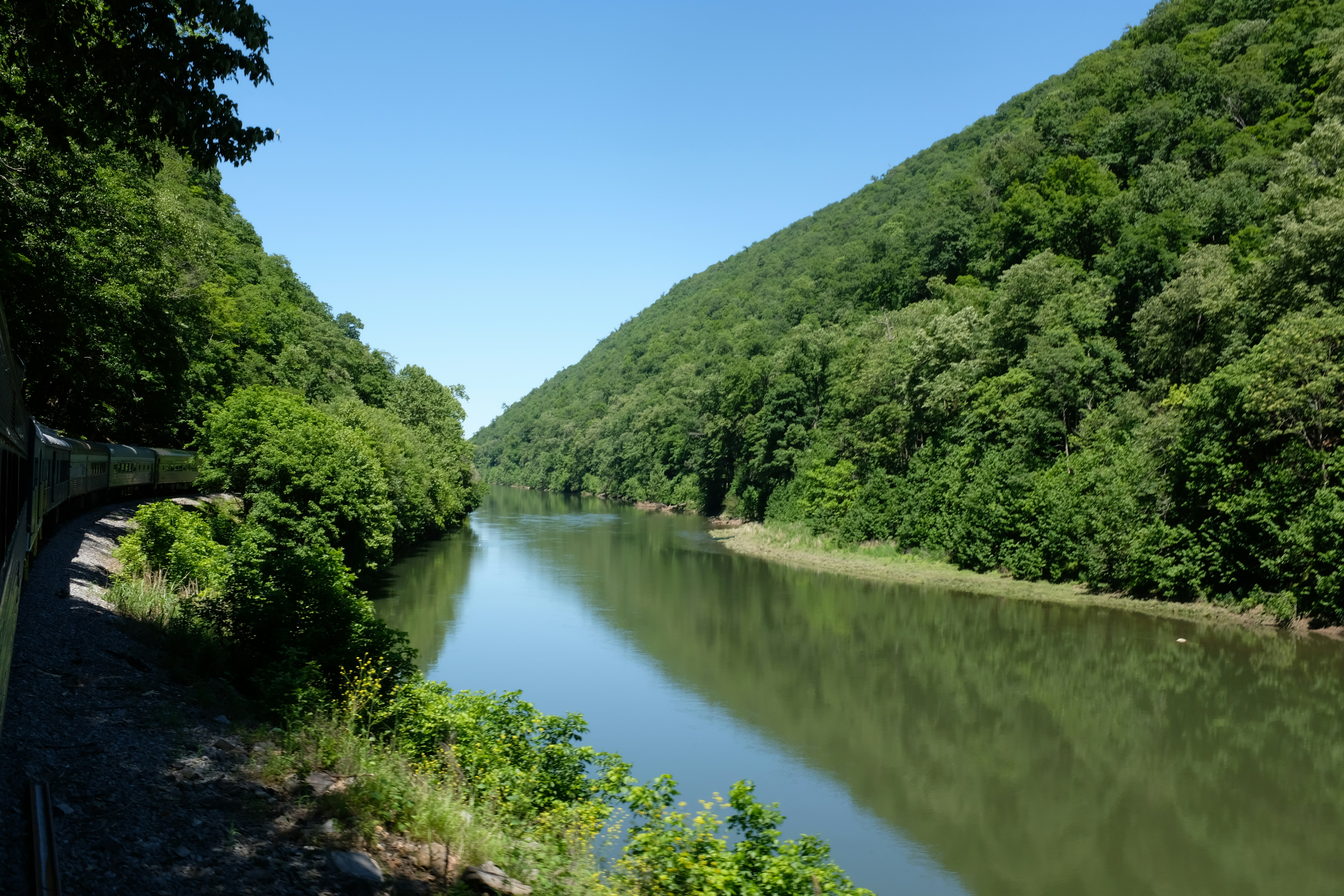 Verdant Channel: Sunlit Rivermeadow Between Forested Ridges