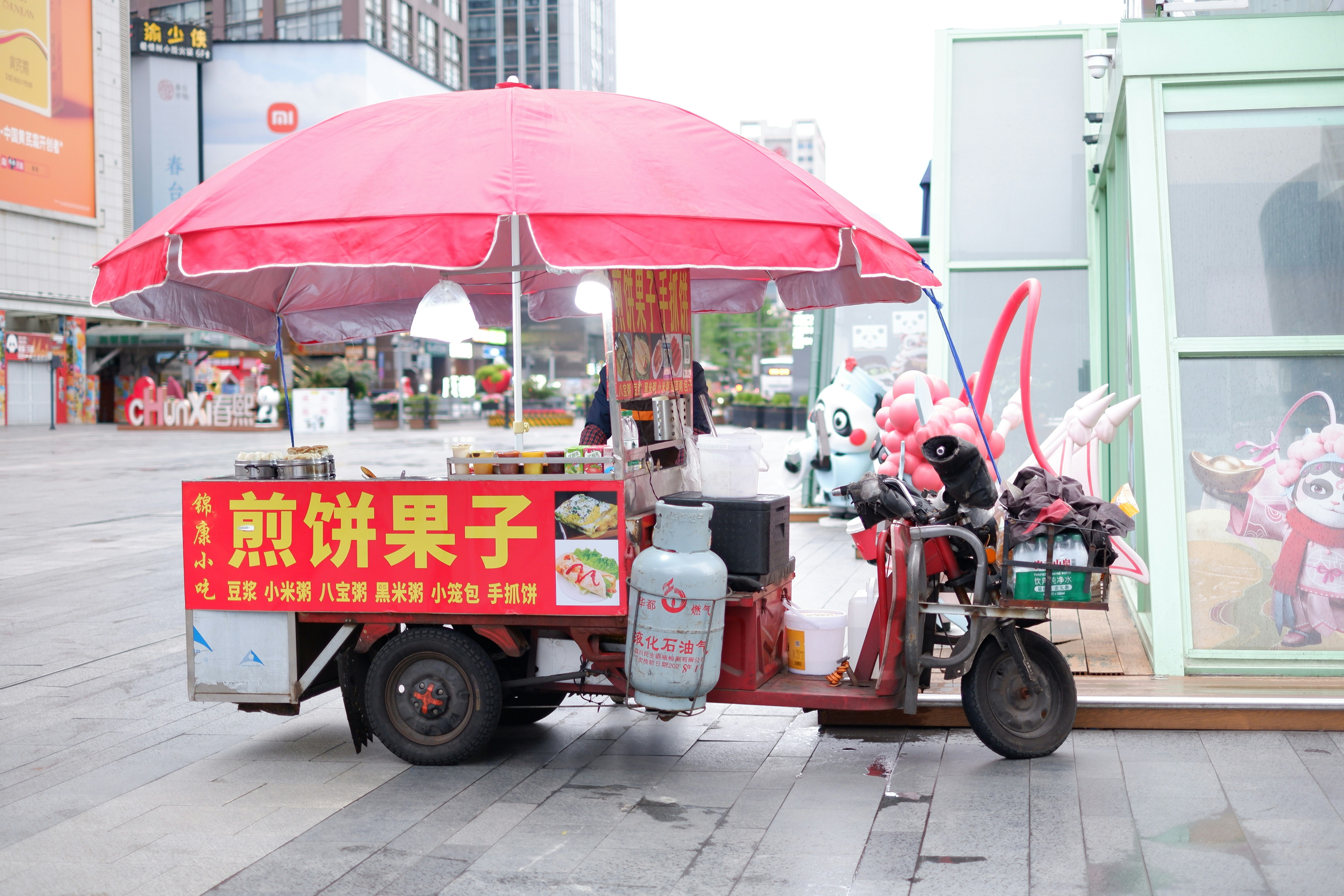 Red umbrella cart of street snacks in a busy urban plaza