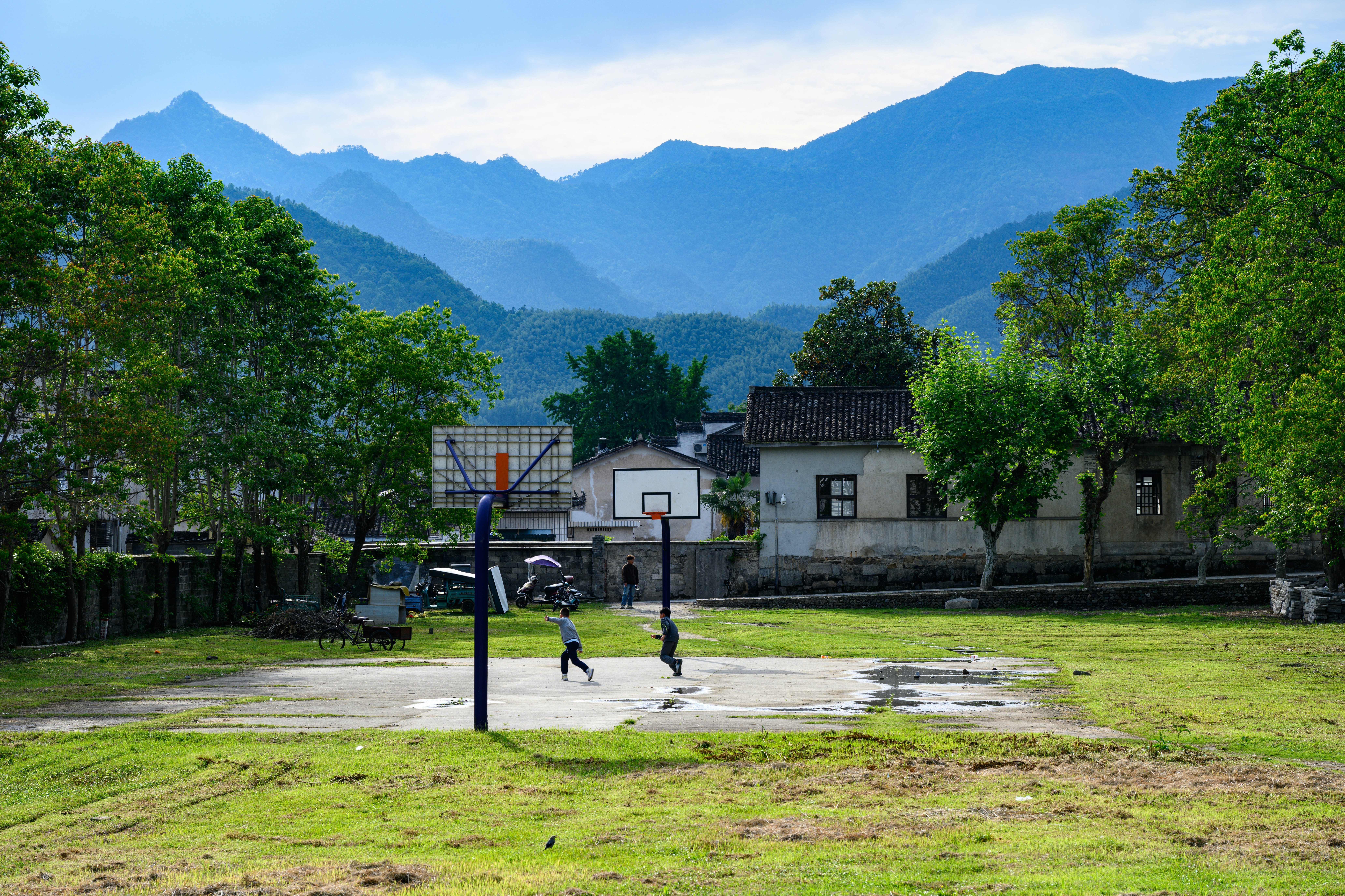 People playing basketball on an outdoor court with mountains.