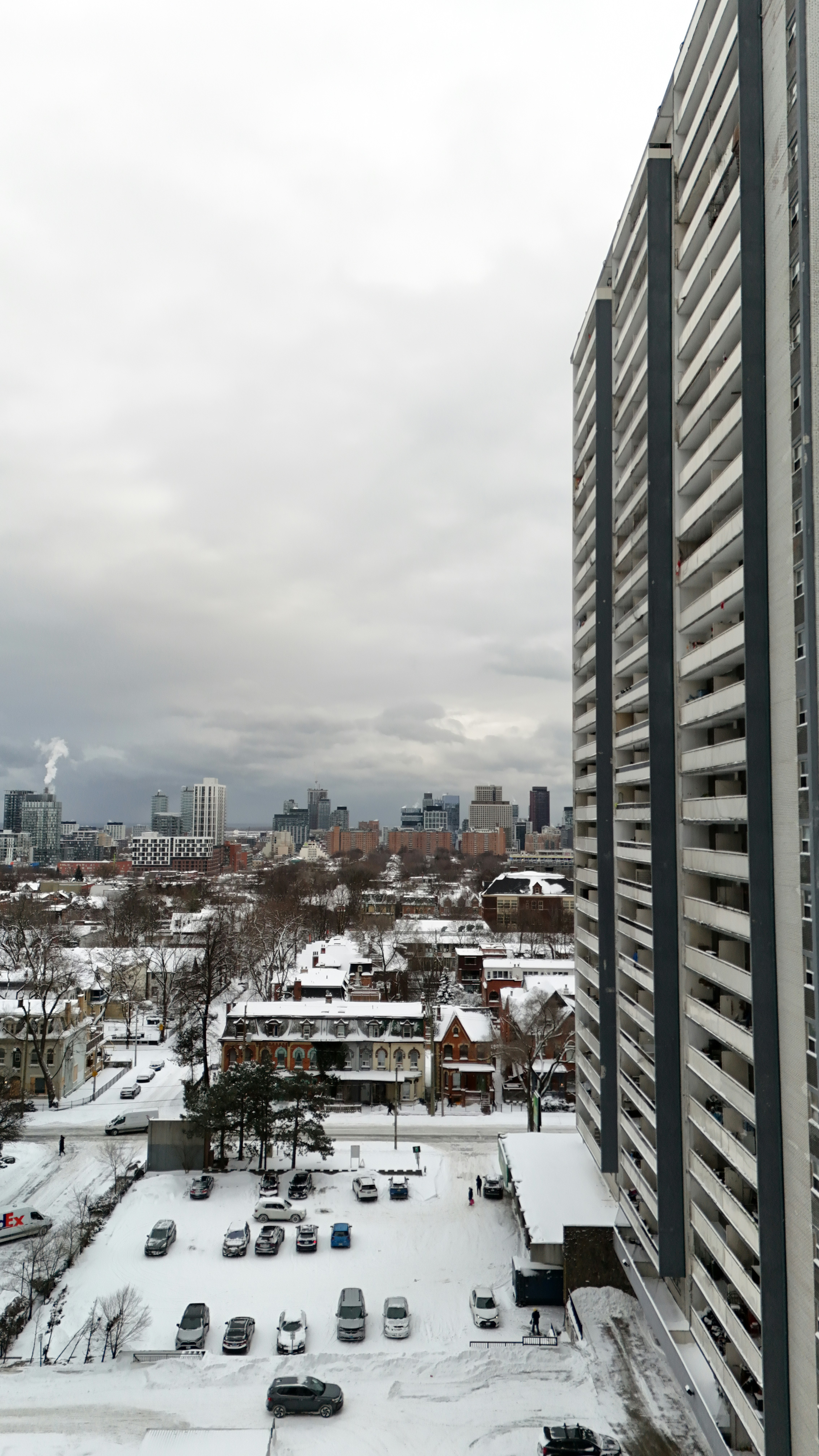 Snow-covered city view with a tall building and cloudy sky.