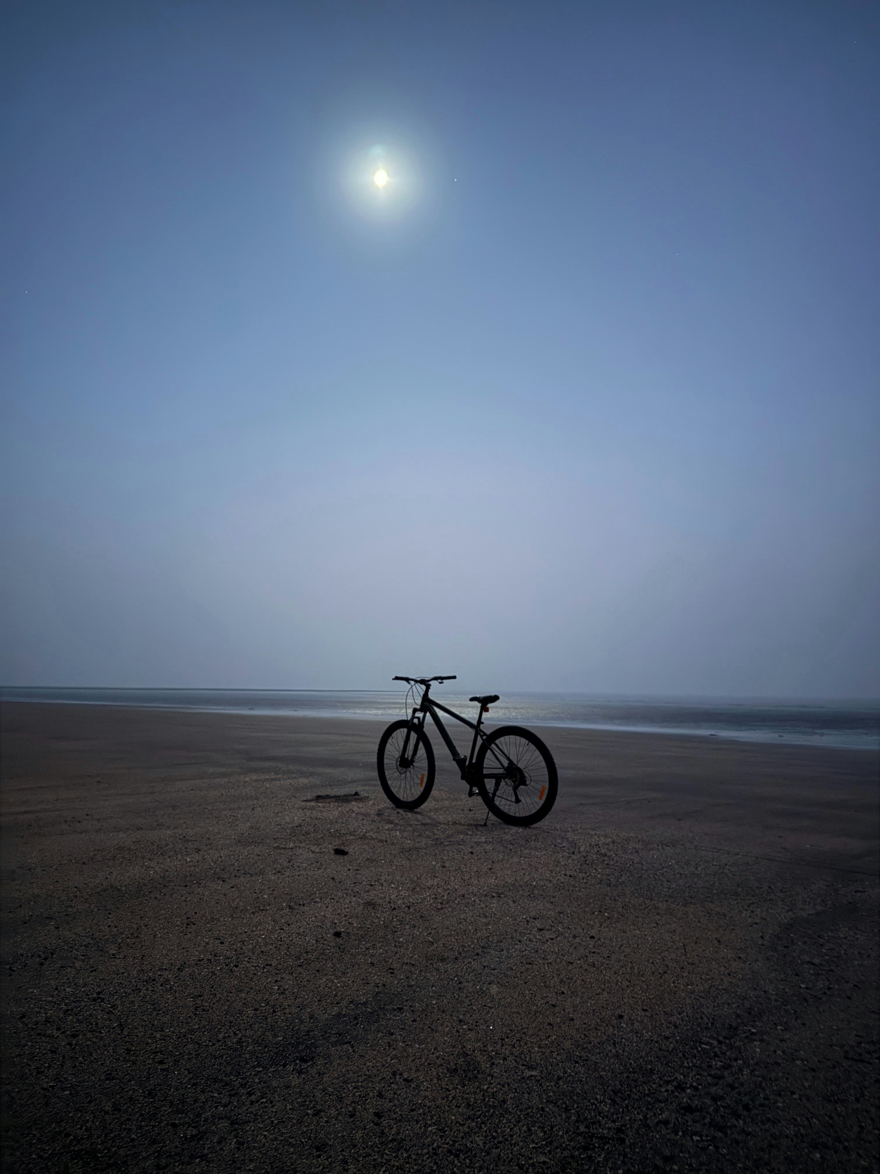 Solitary bicycle on a misty beach under a glowing sky.