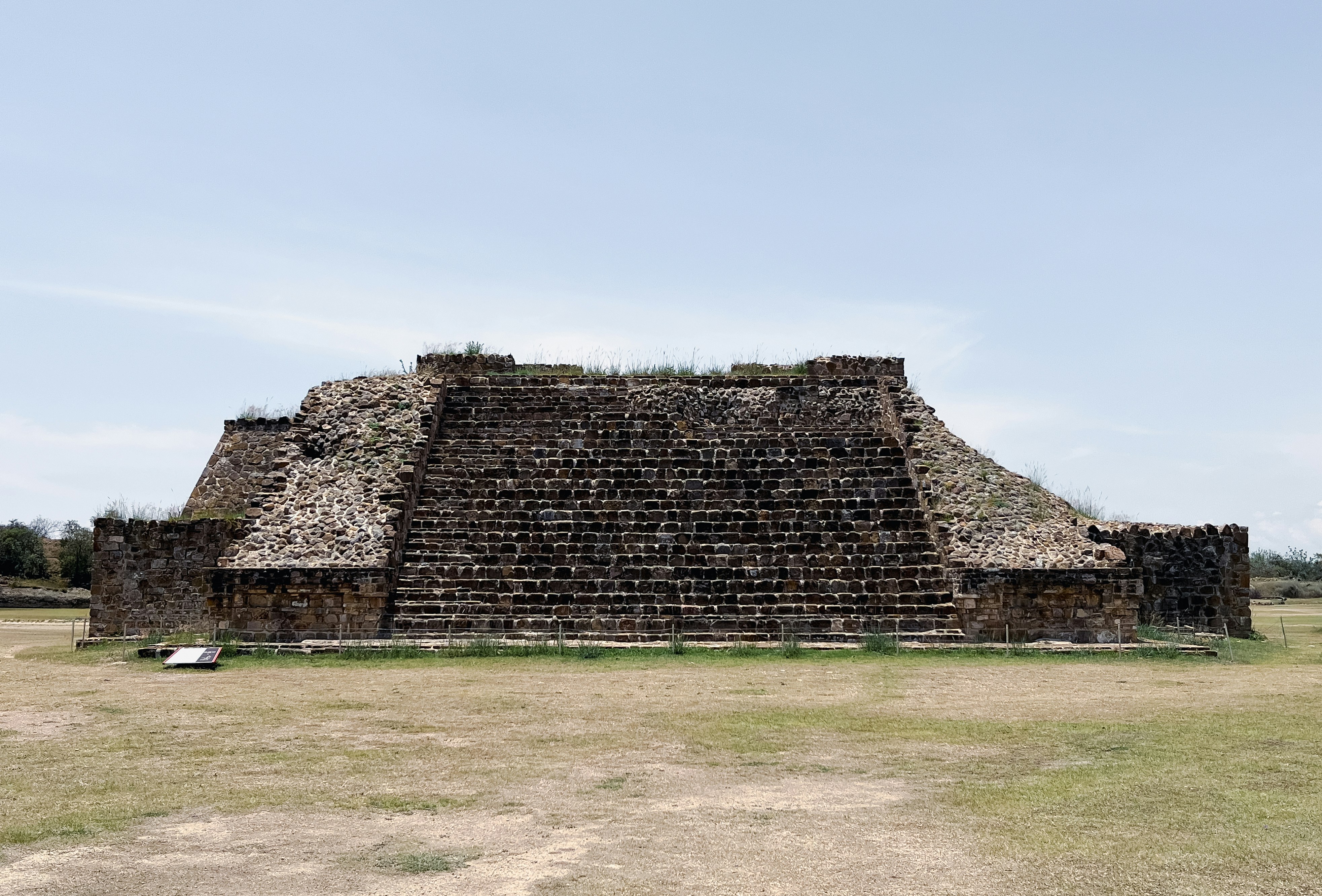 Stepped stone pyramid ruins in an open field.