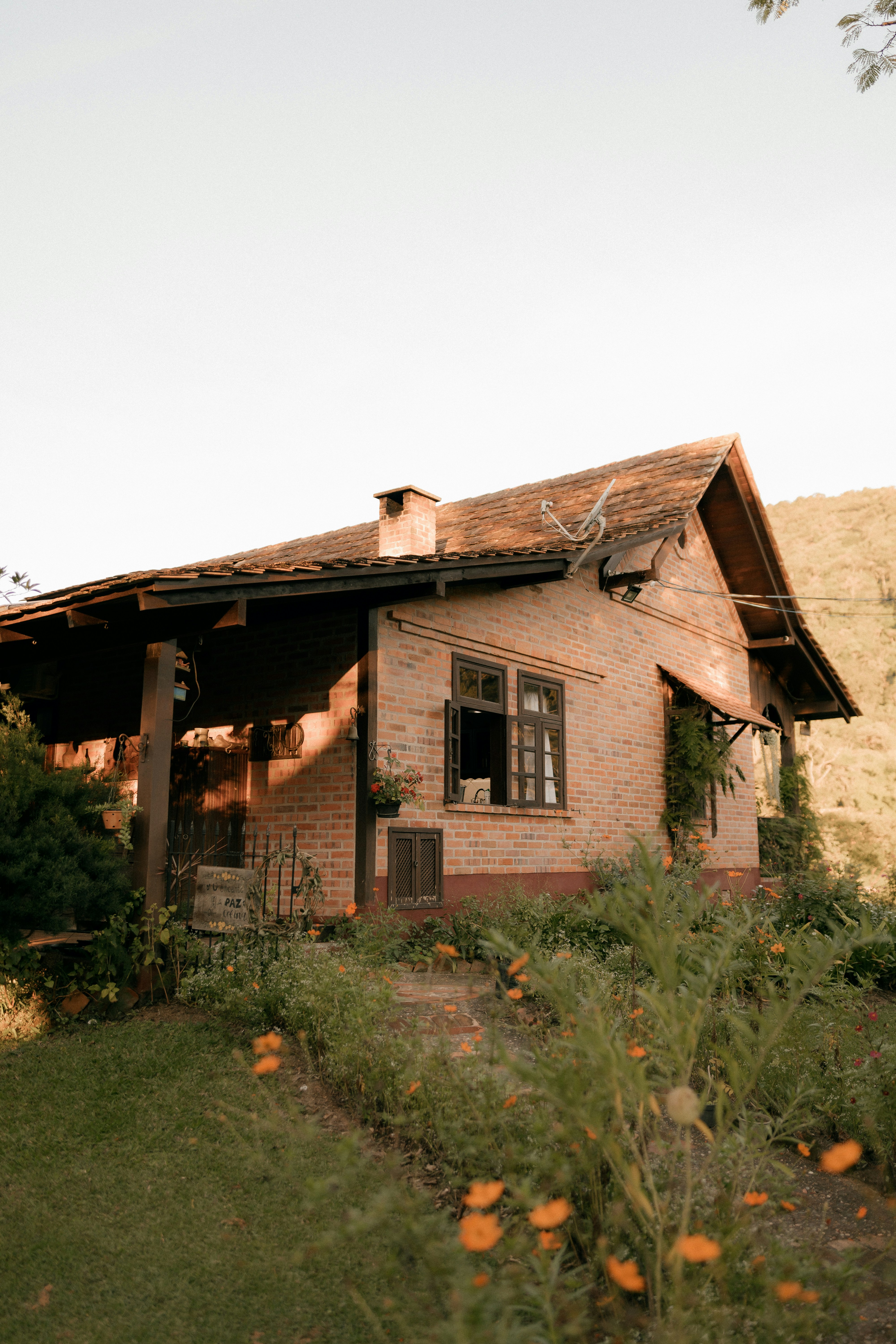 A rustic brick house surrounded by lush greenery and flowers.