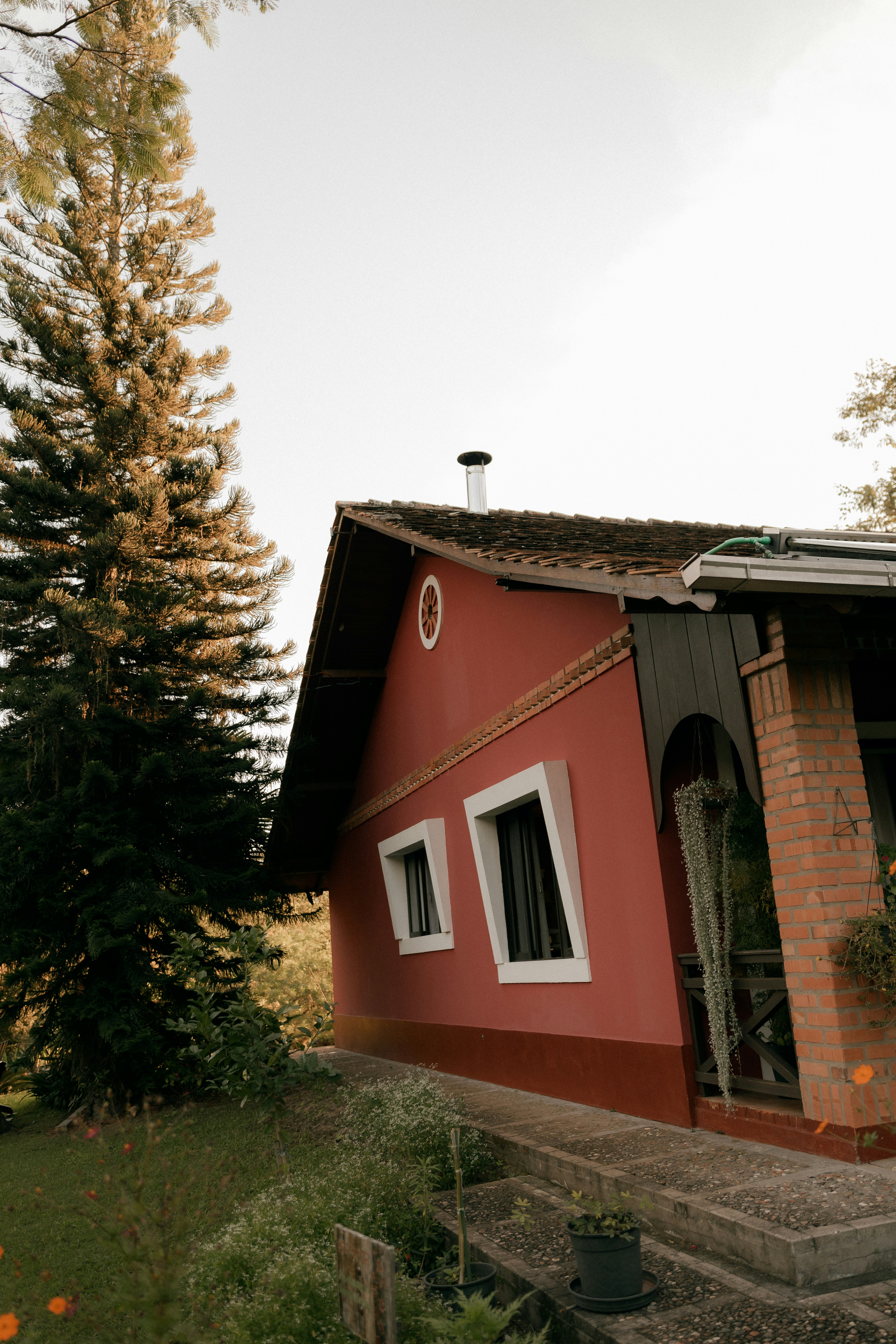 Red-walled Cottage with slanted Roof and Chimney Framed by Pine