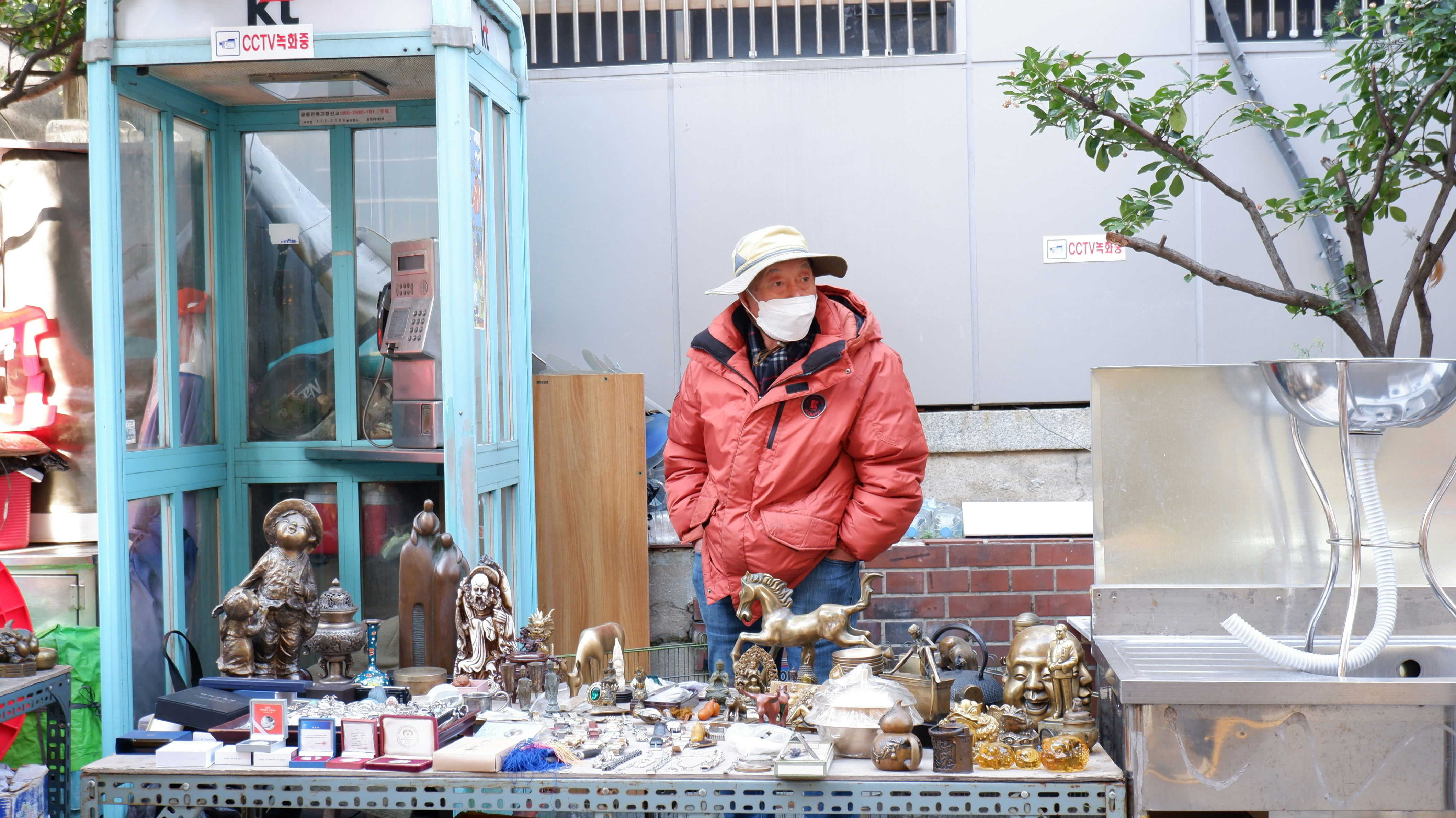 Red Jacket Vendor at a Market Stand Surrounded by Handcrafted Statues