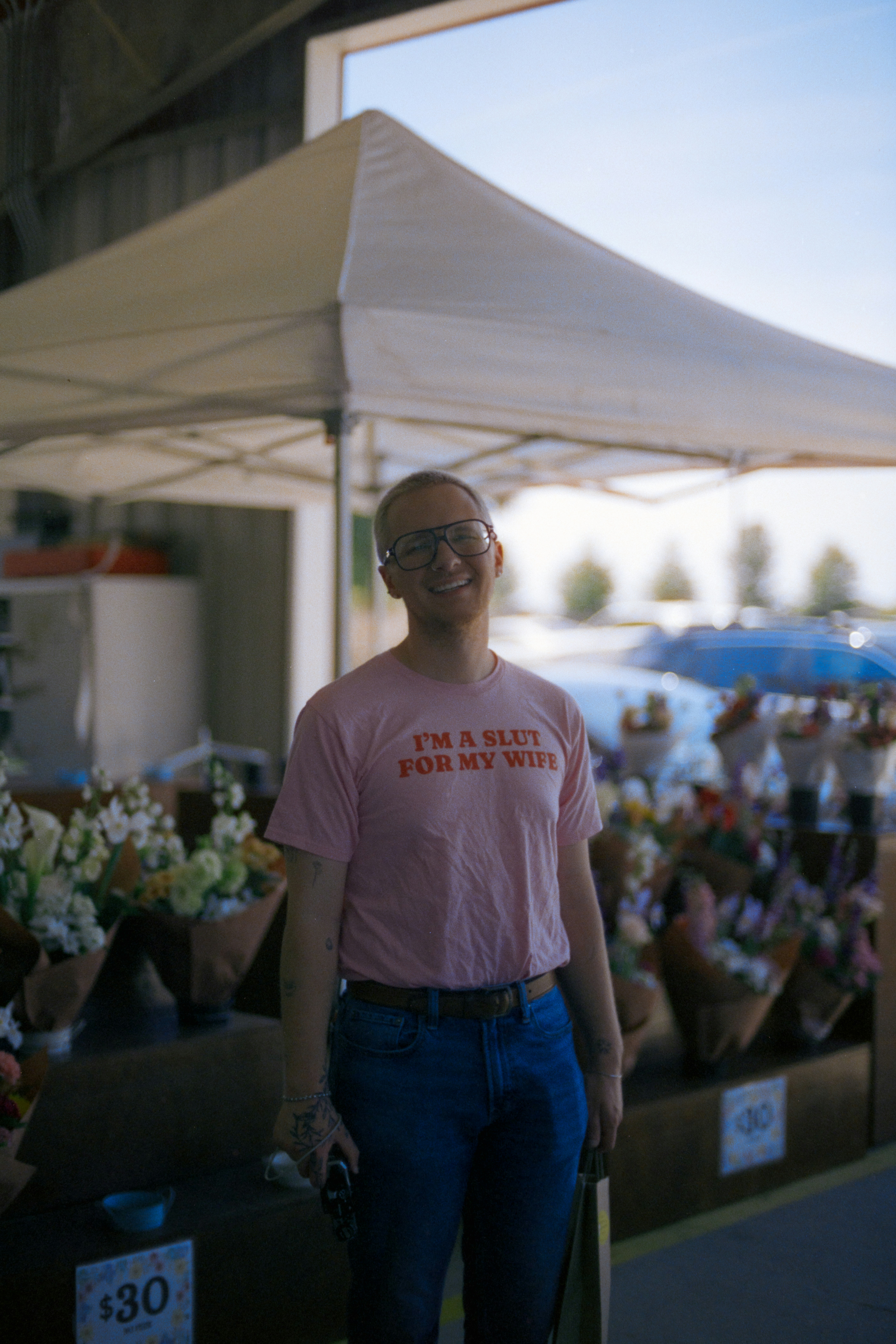 Smiling man in pink t-shirt at outdoor flower market.