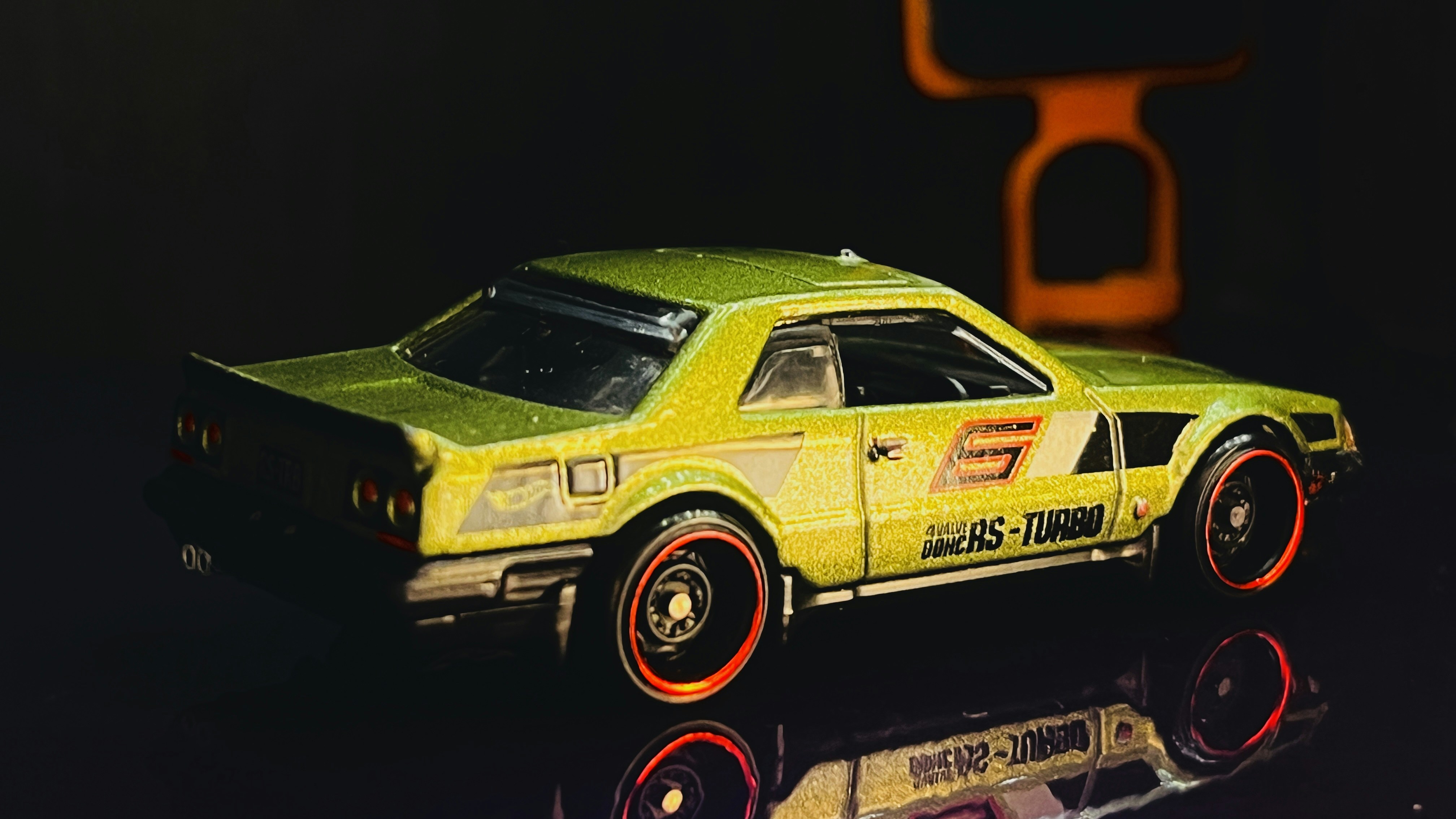 Neon-green toy coupe with red-outline wheels under soft glow
