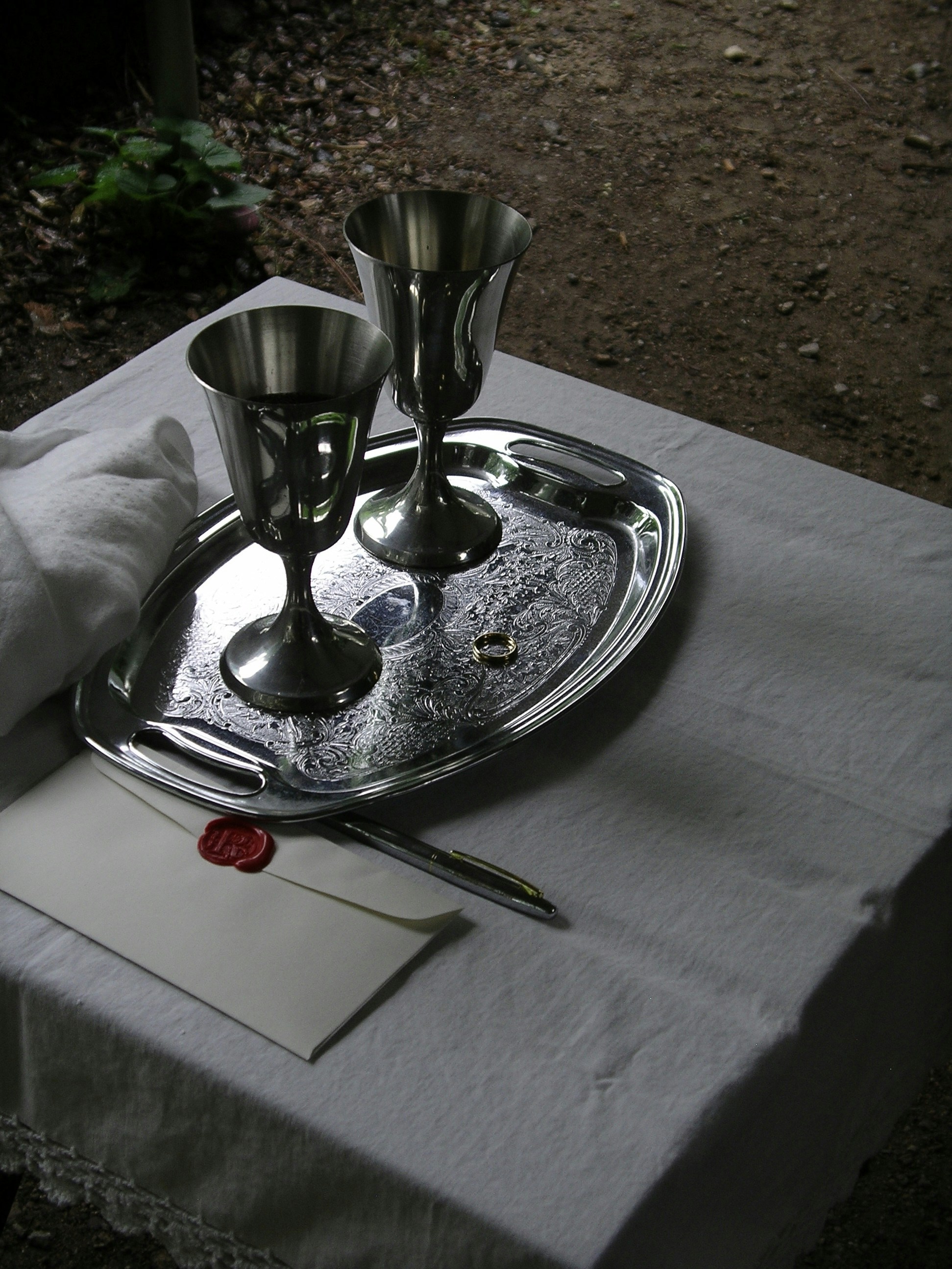 Silver goblets, ring, and sealed envelope on a white tablecloth.