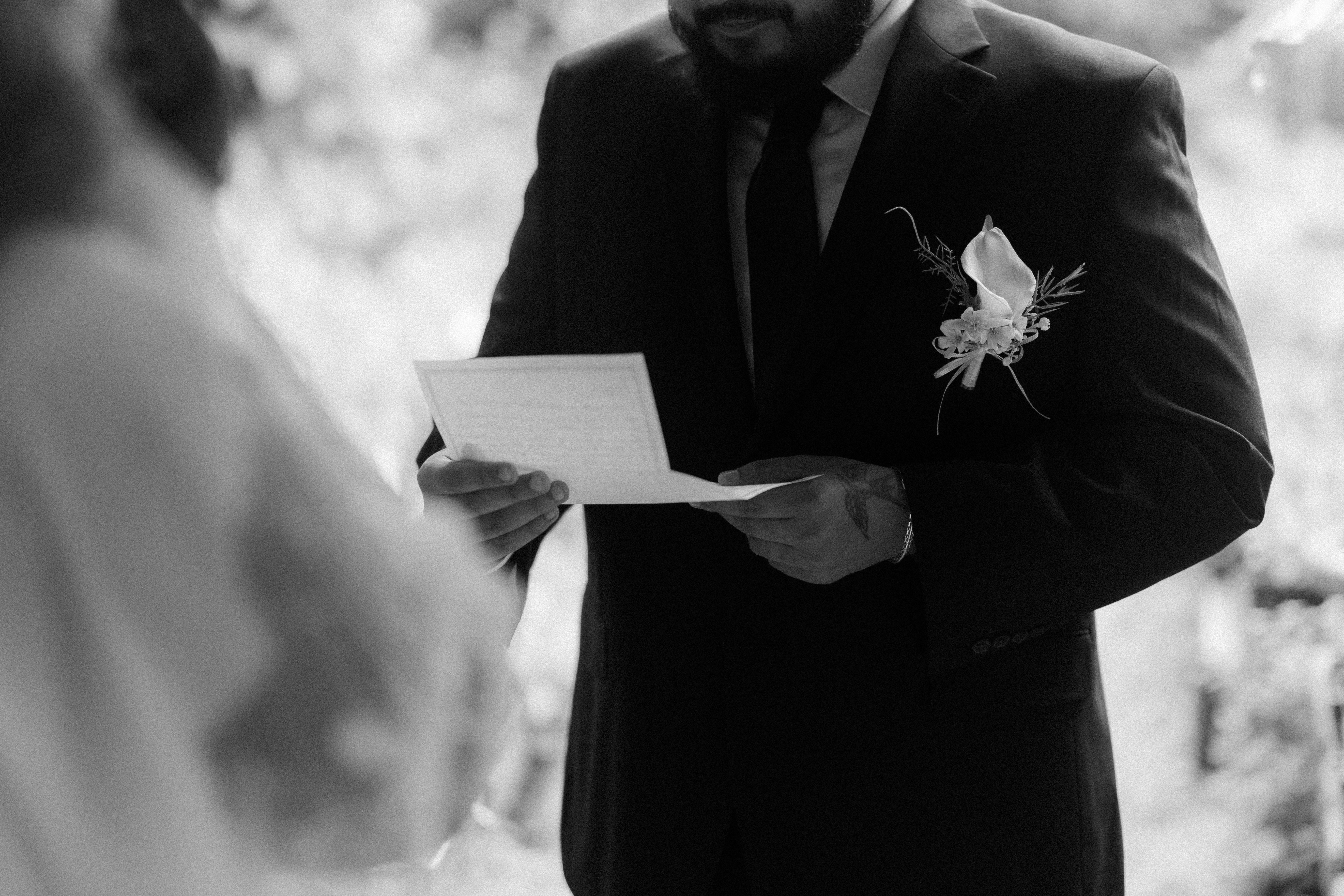 Man in suit reading vows during a ceremony.