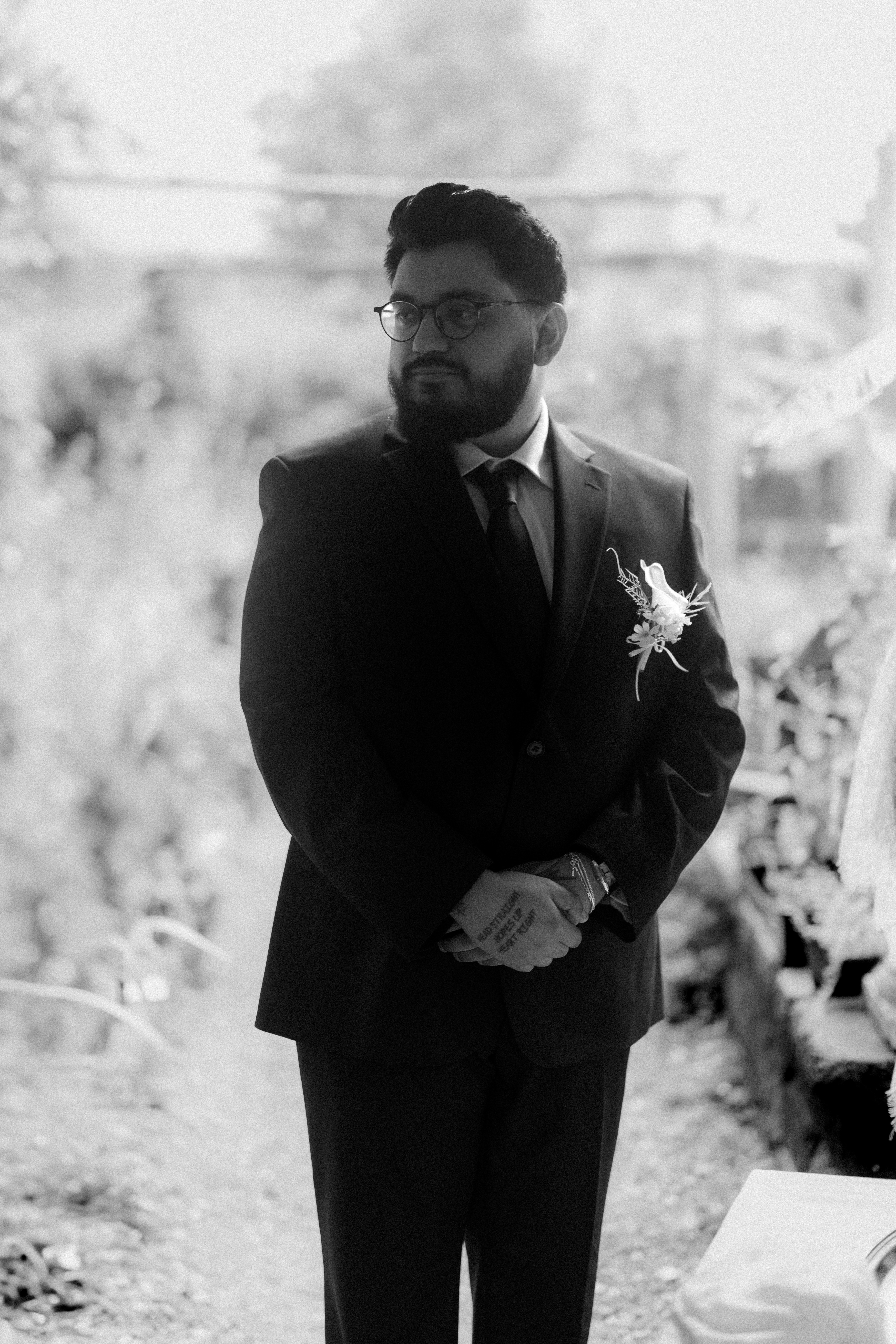 Bearded man in suit and glasses stands outdoors.