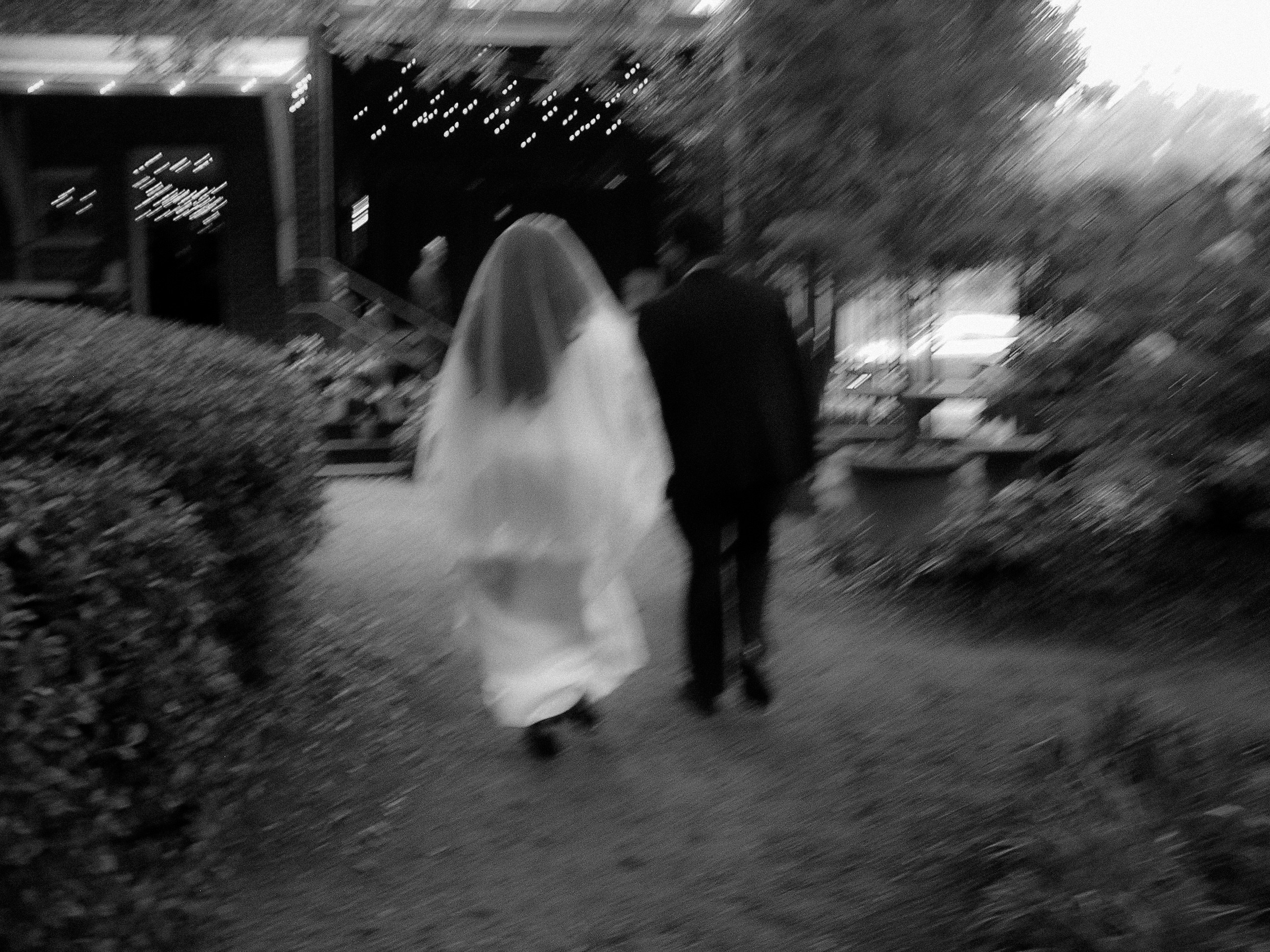 A bride and groom walking away in a blurry garden.