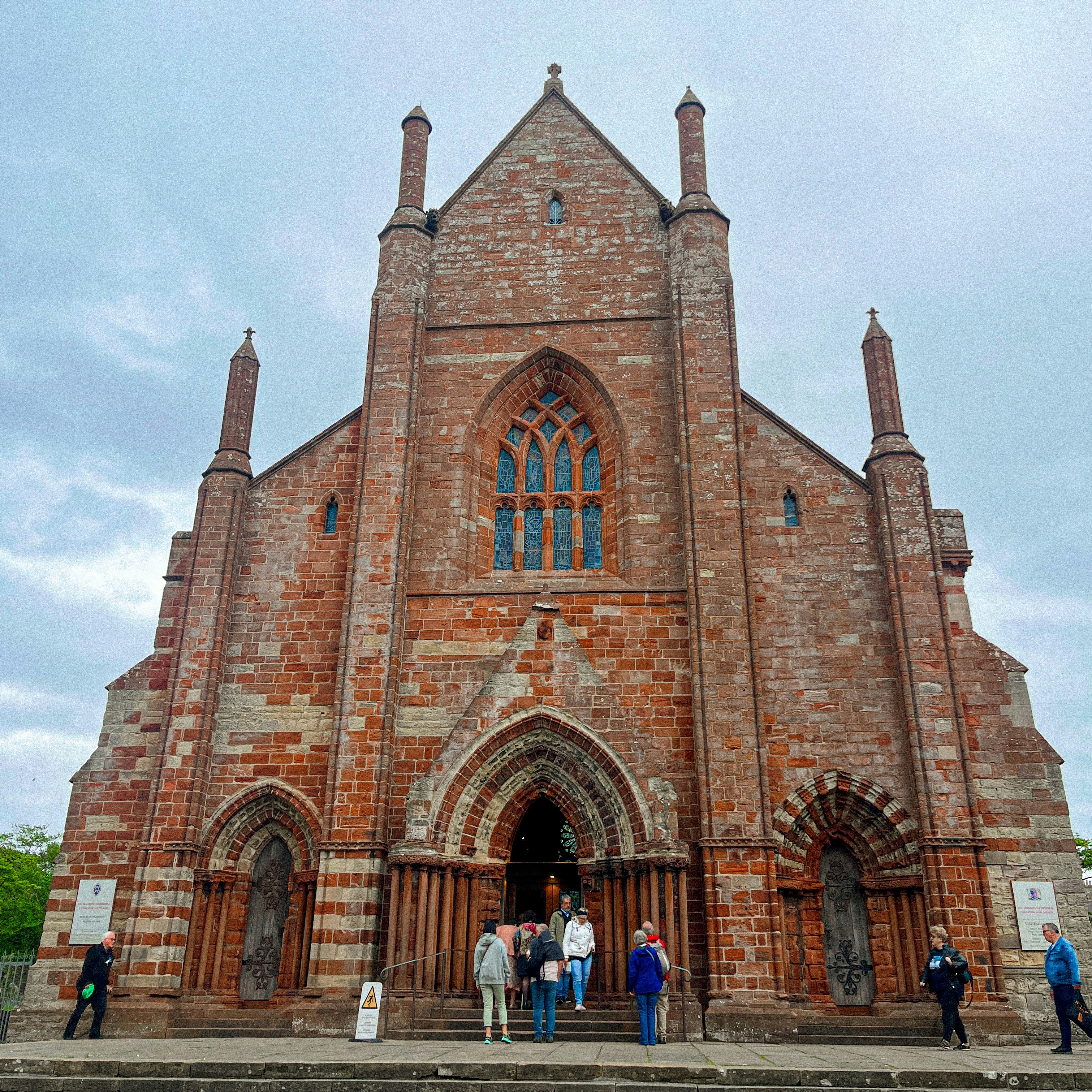 Historic red brick church with arched entrances and people outside.