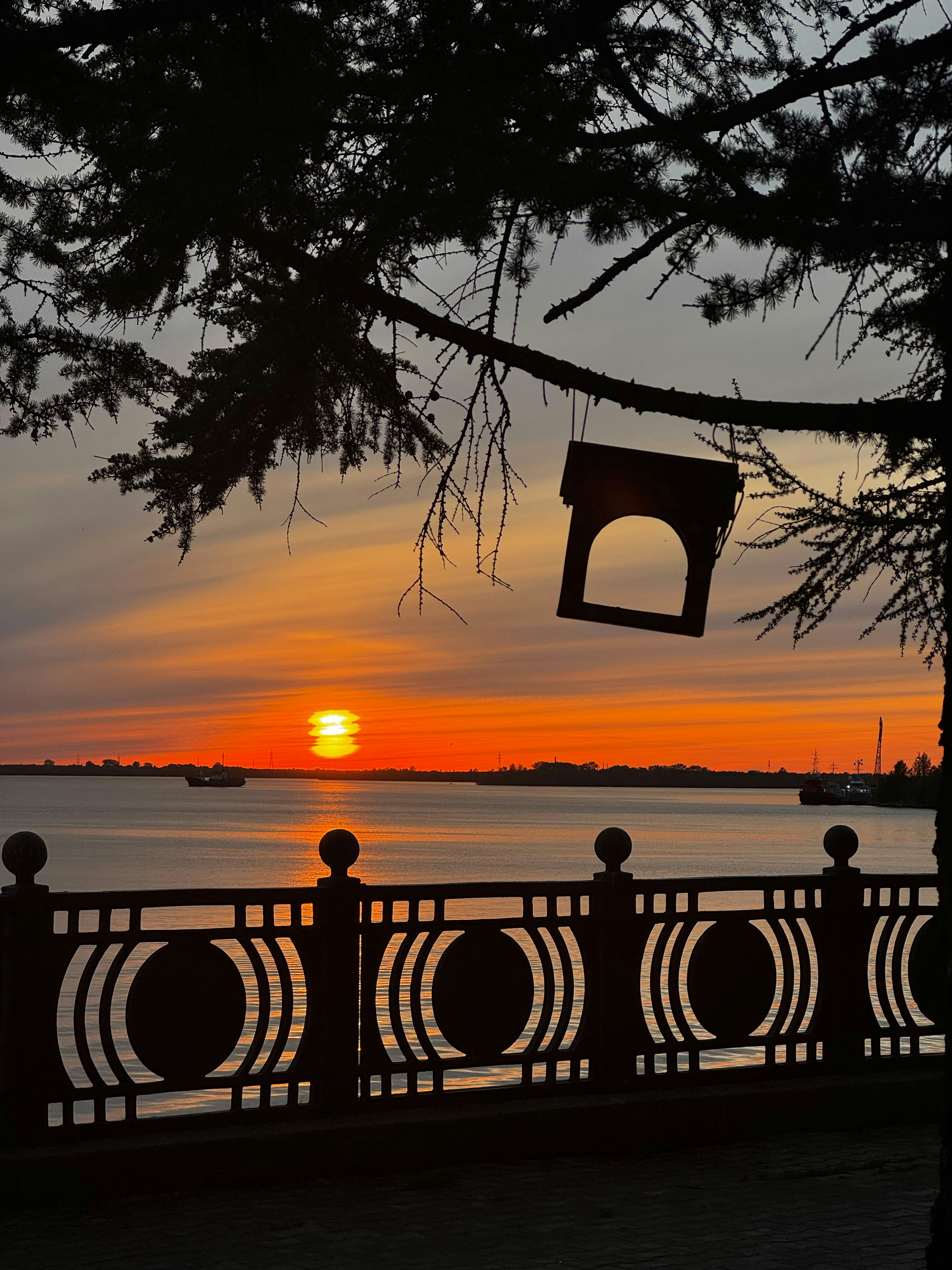 Sunset over the railing: silhouette of a hanging swing against a tranquil river