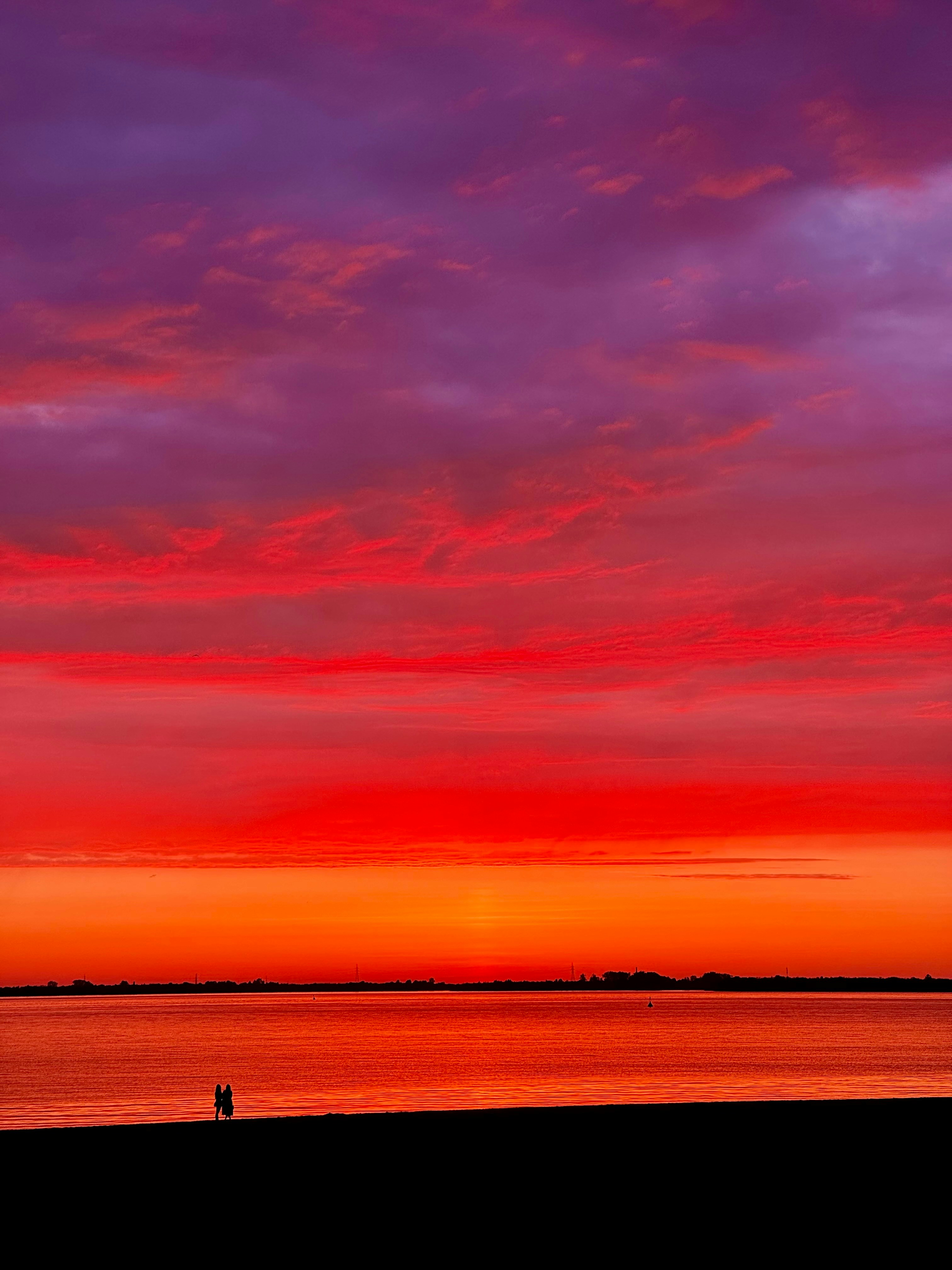 Dramatic red and purple sunset over calm water with silhouettes.
