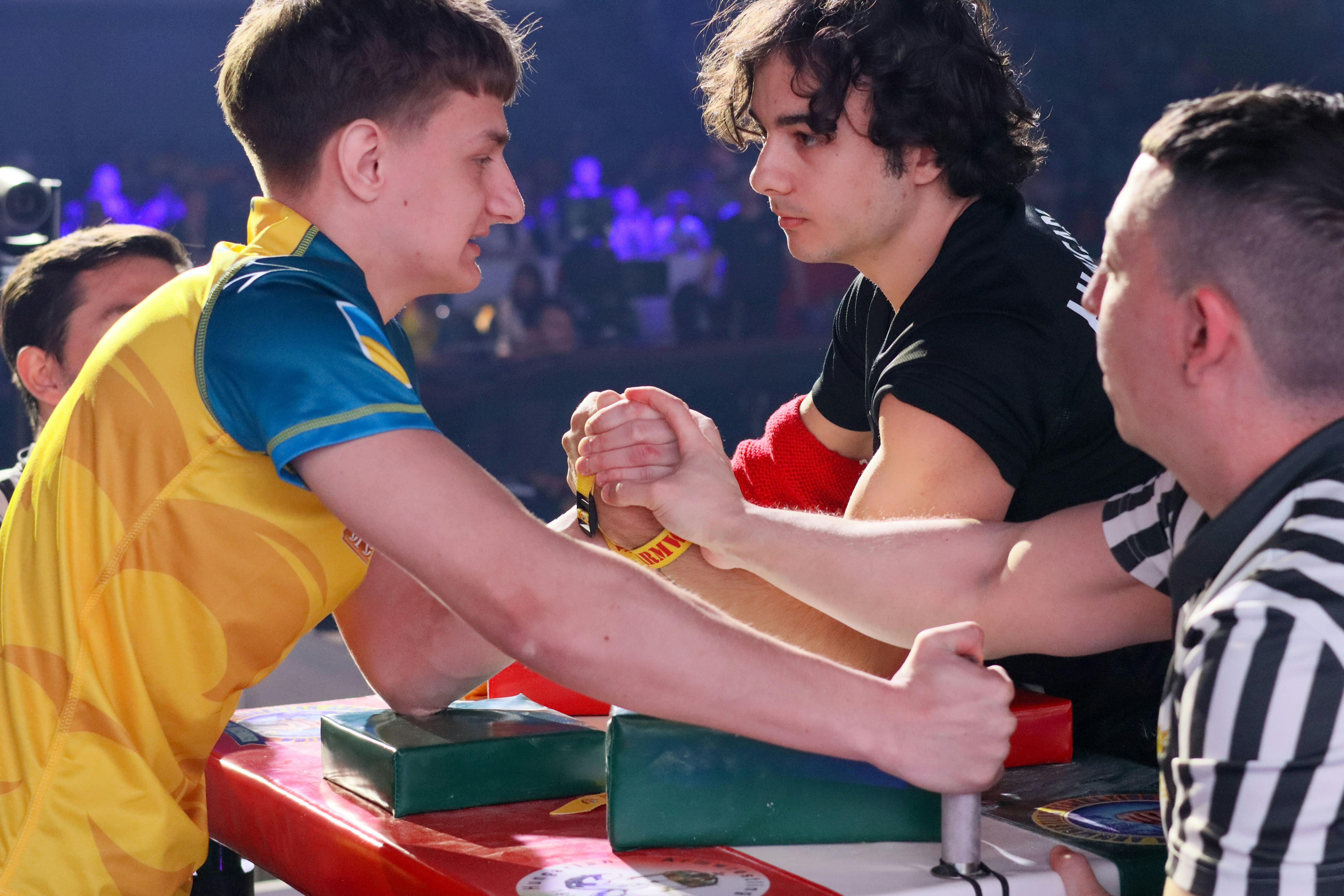 Two young men arm wrestling with a referee watching intently.