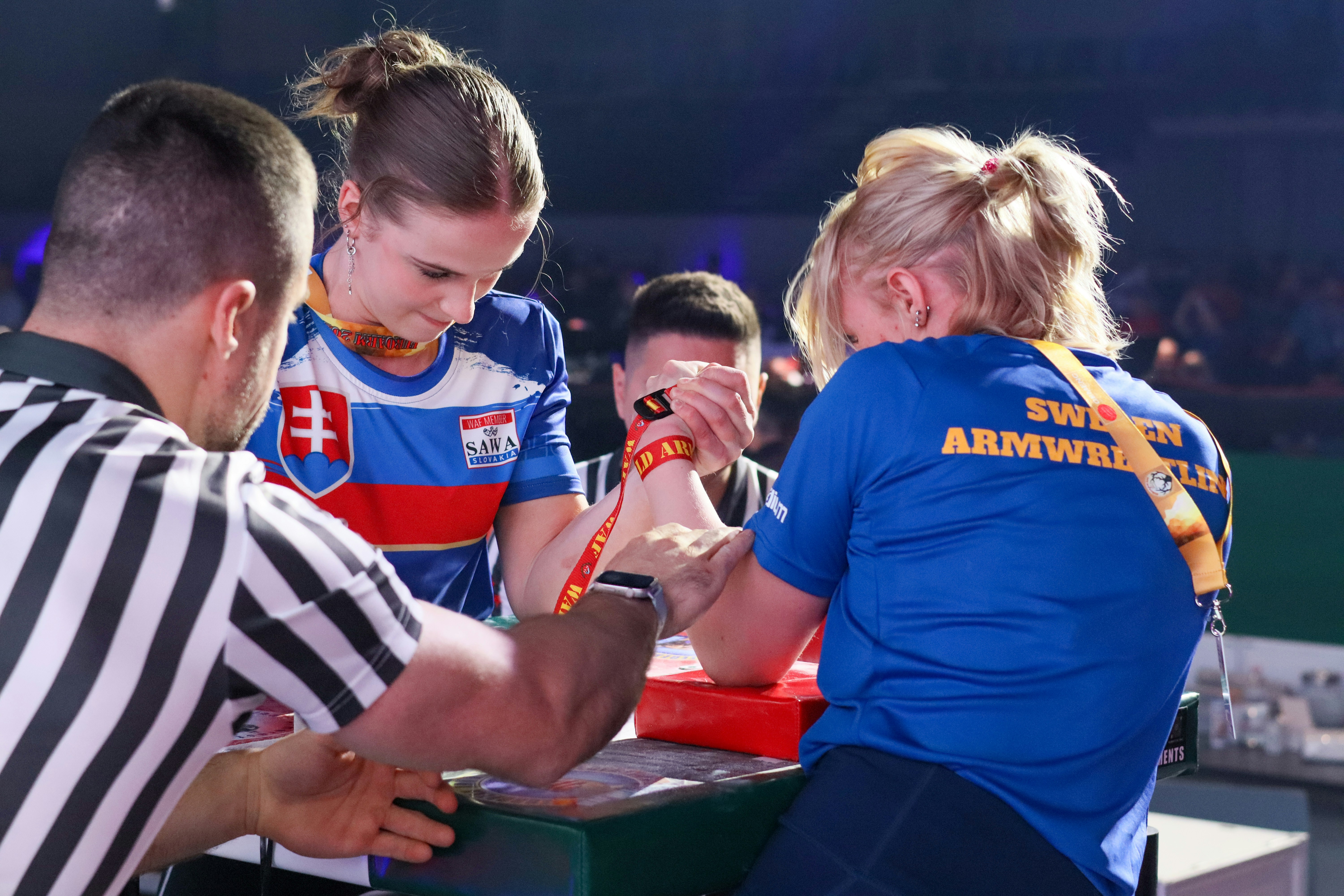 Two women arm wrestling with a referee present.
