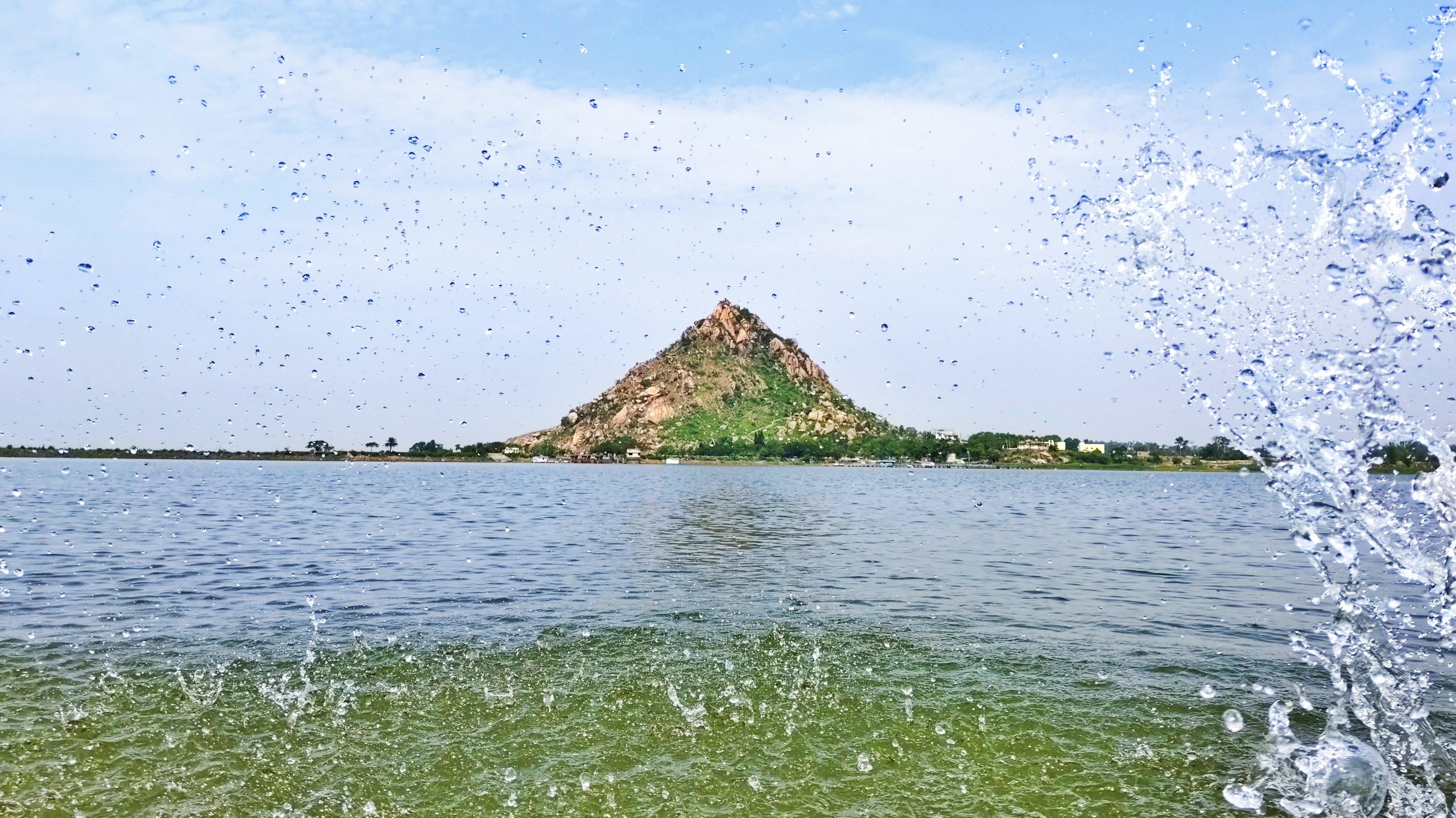 Green Peak Rising from a Serene Lake with Water Sprays