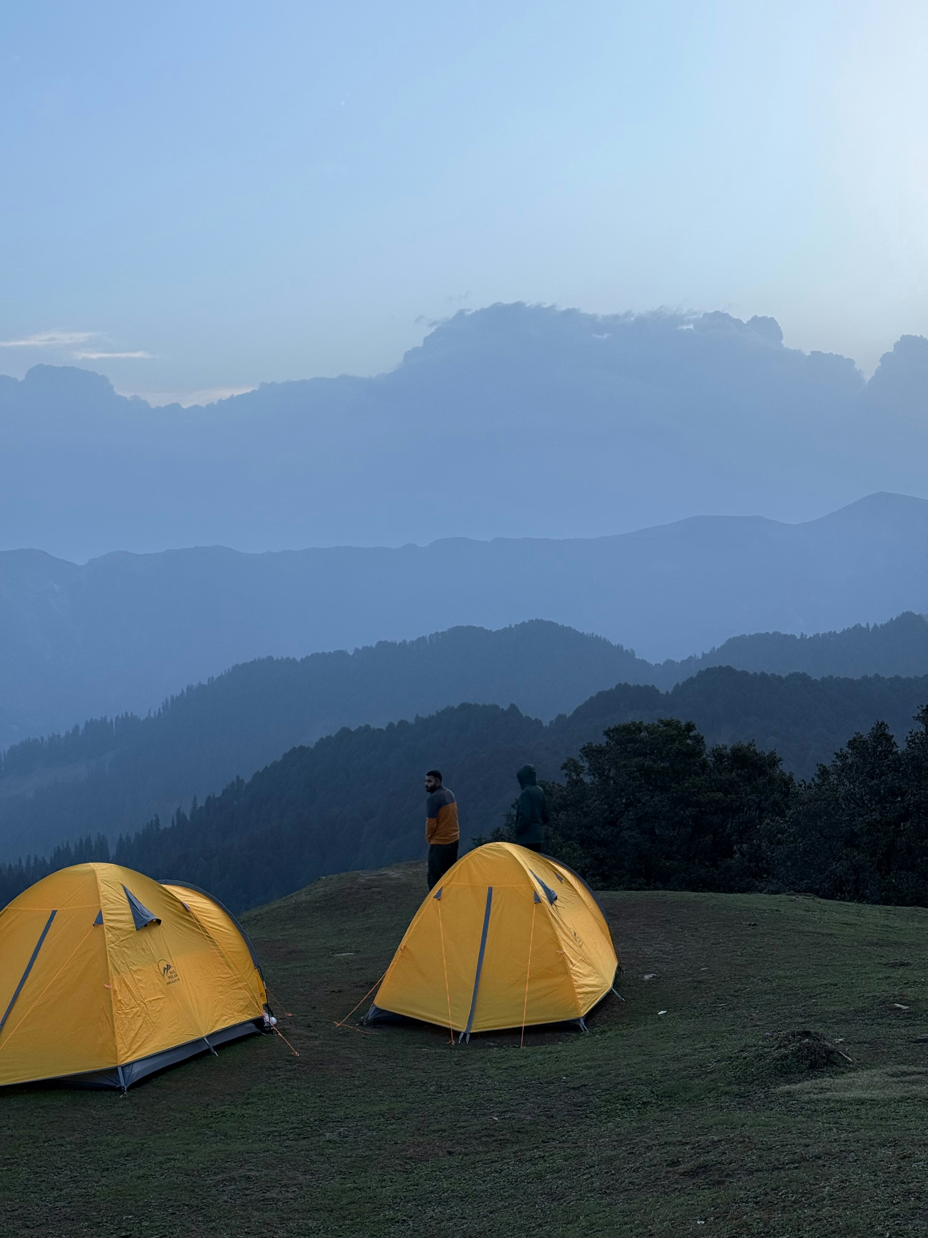 Camping with yellow tents and a person overlooking blue mountains.
