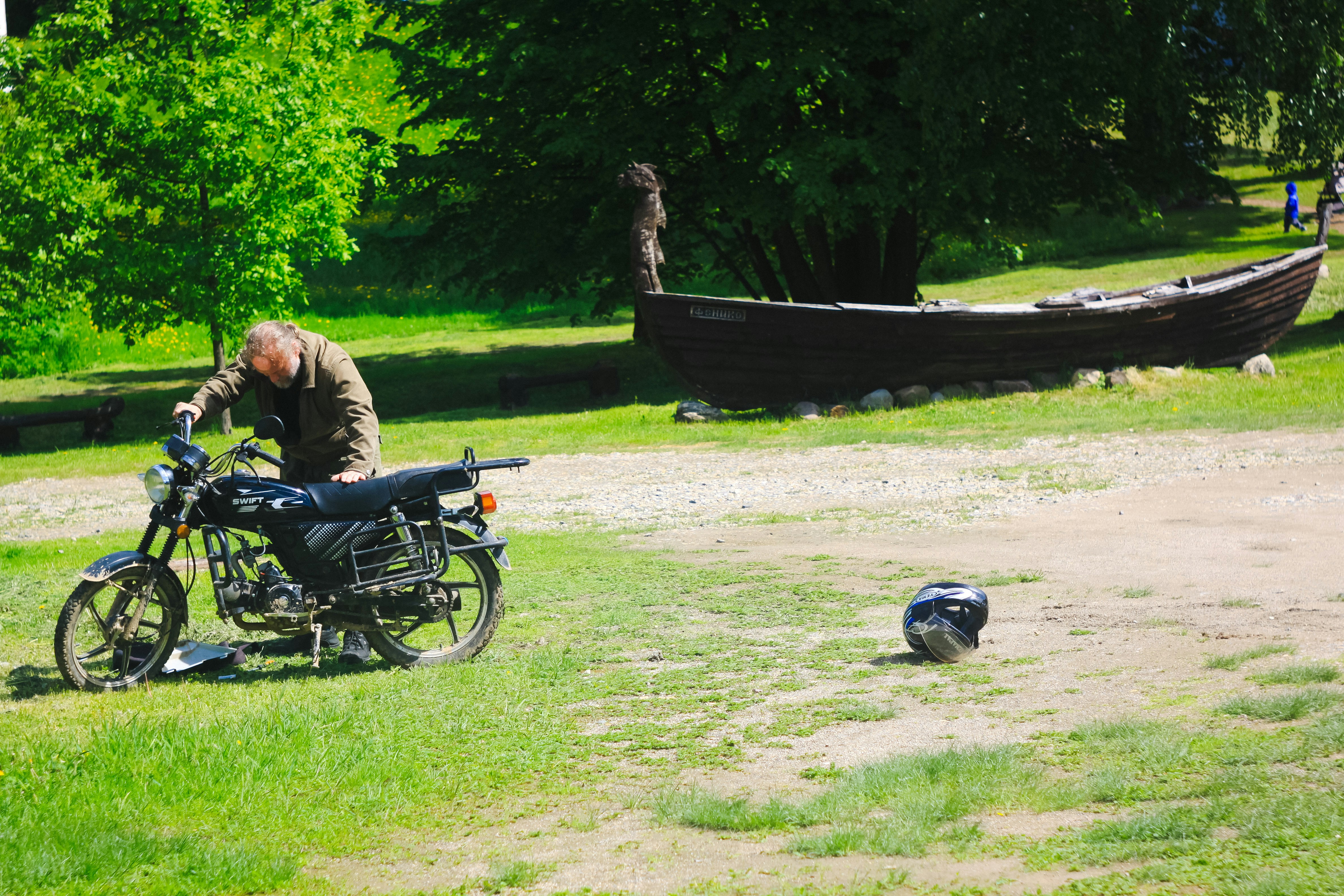 Man and vintage motorcycle anchor a sunlit grassy field
