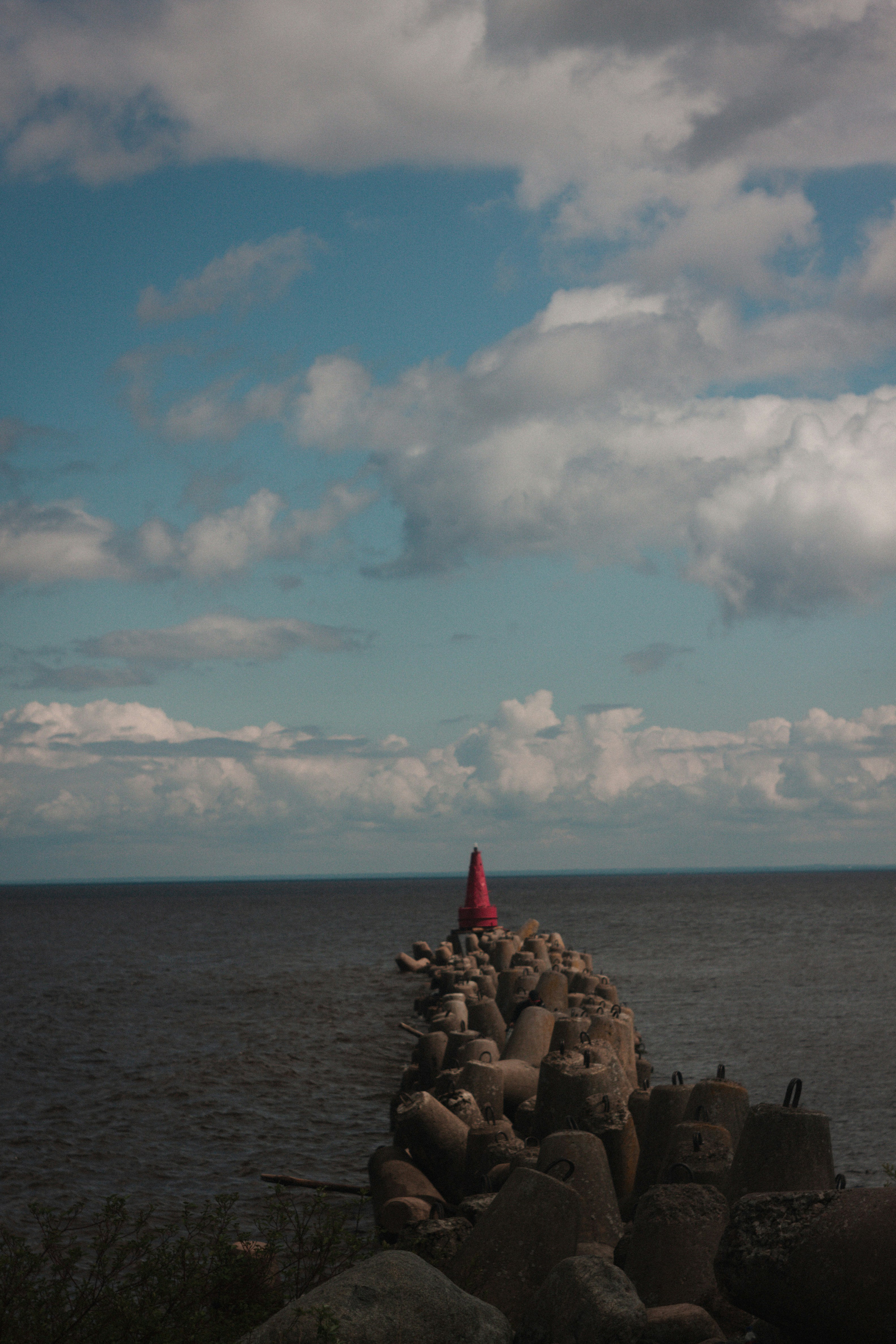 Red beacon at the end of a stone breakwater against a calm sea