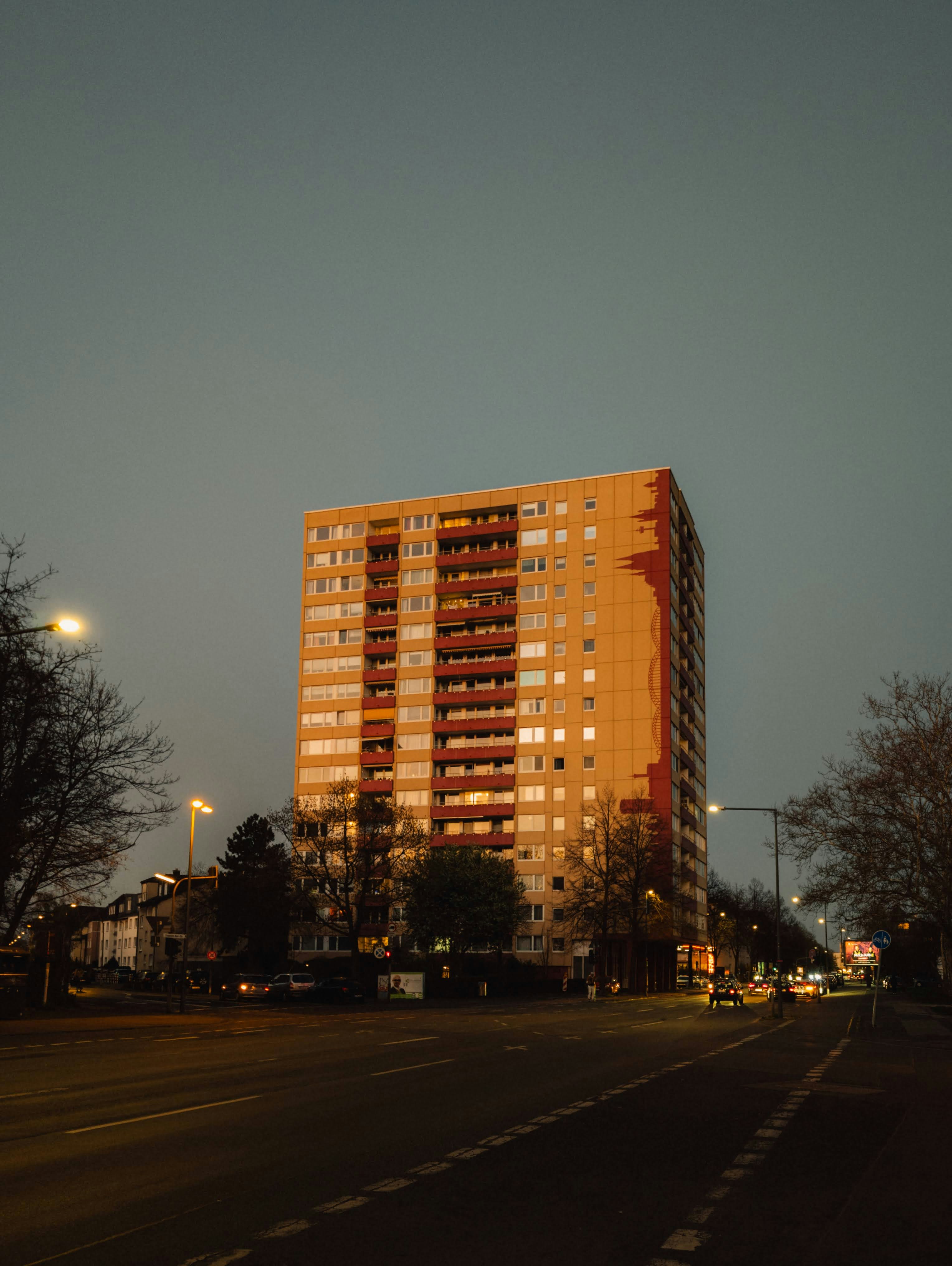 Sunlit apartment tower rising over quiet city street at dusk