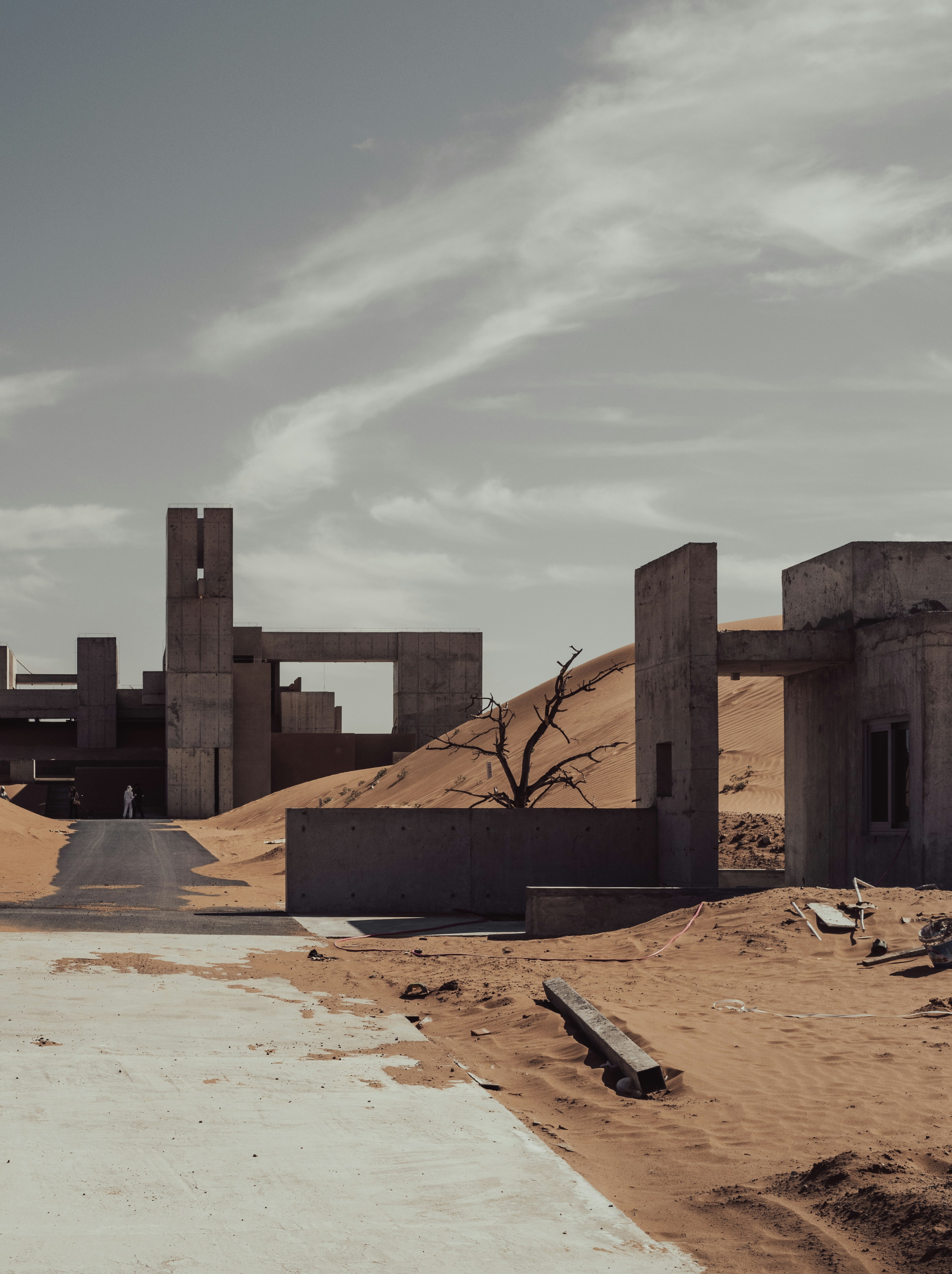 Concrete ruins rise from desert dunes under a calm sky