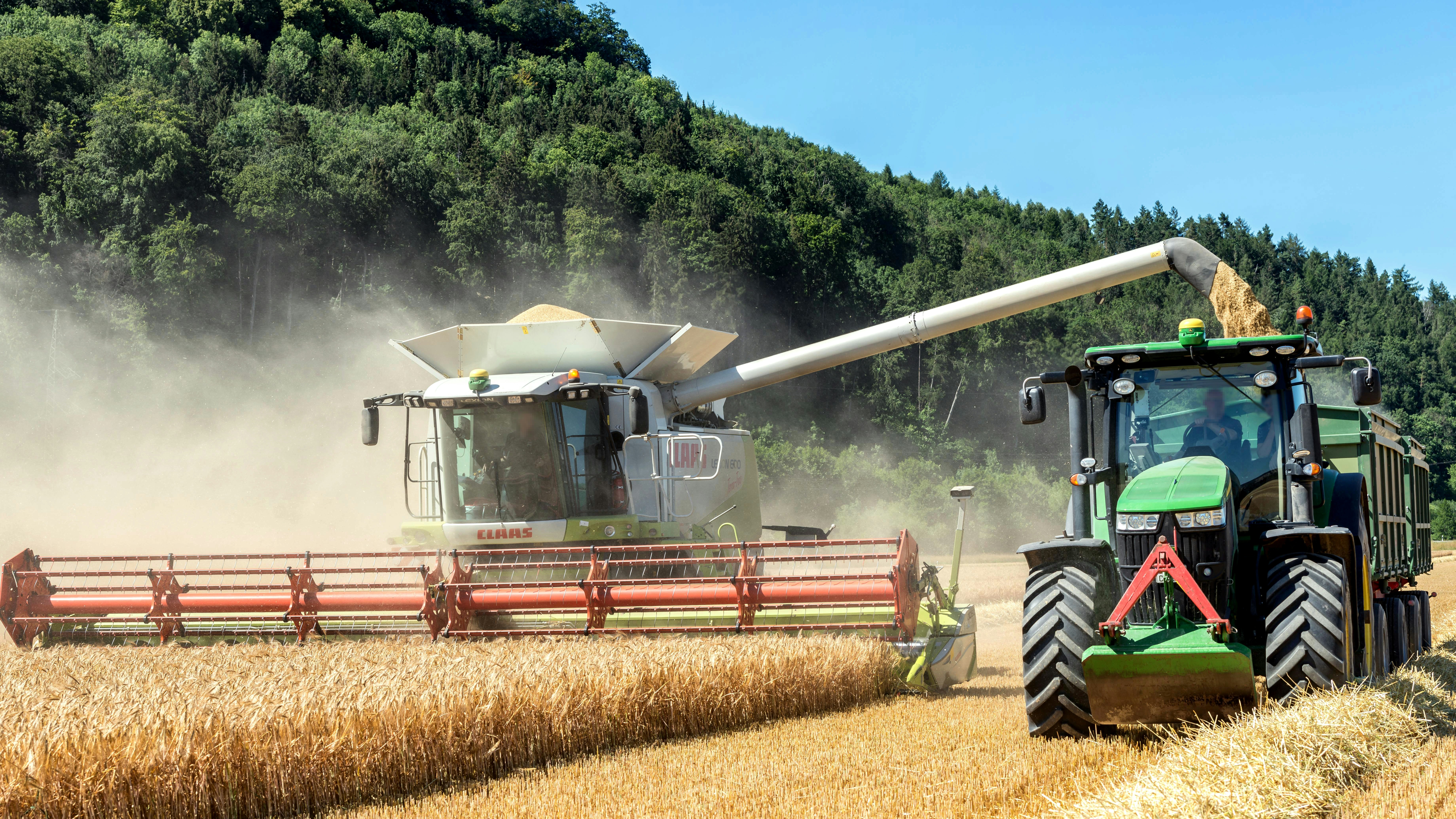 Dust and Harvest: A Green Tractor Leads the Way Through a Golden Field