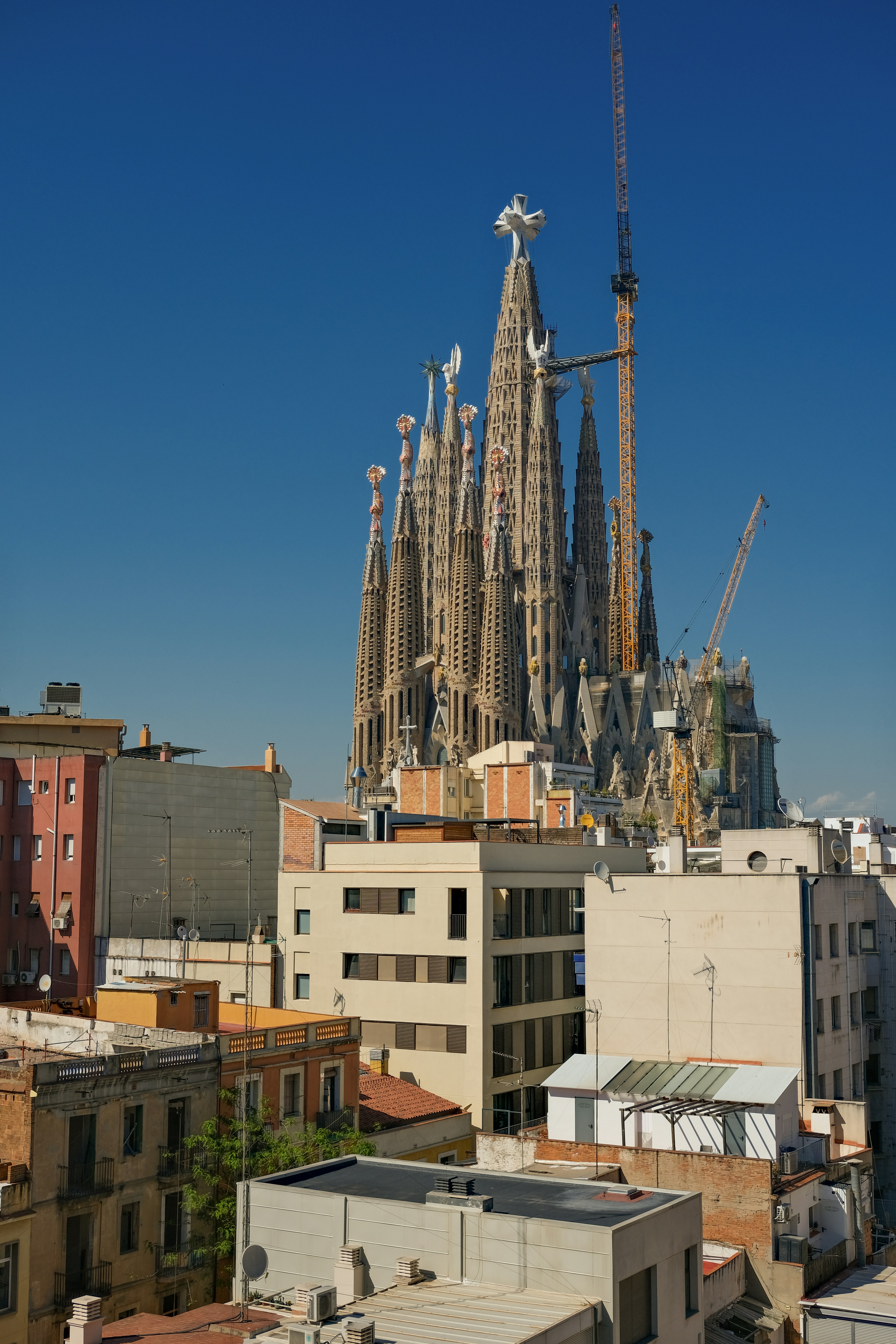 Sagrada silhouettes over the city: cranes and spires against a clear blue sky