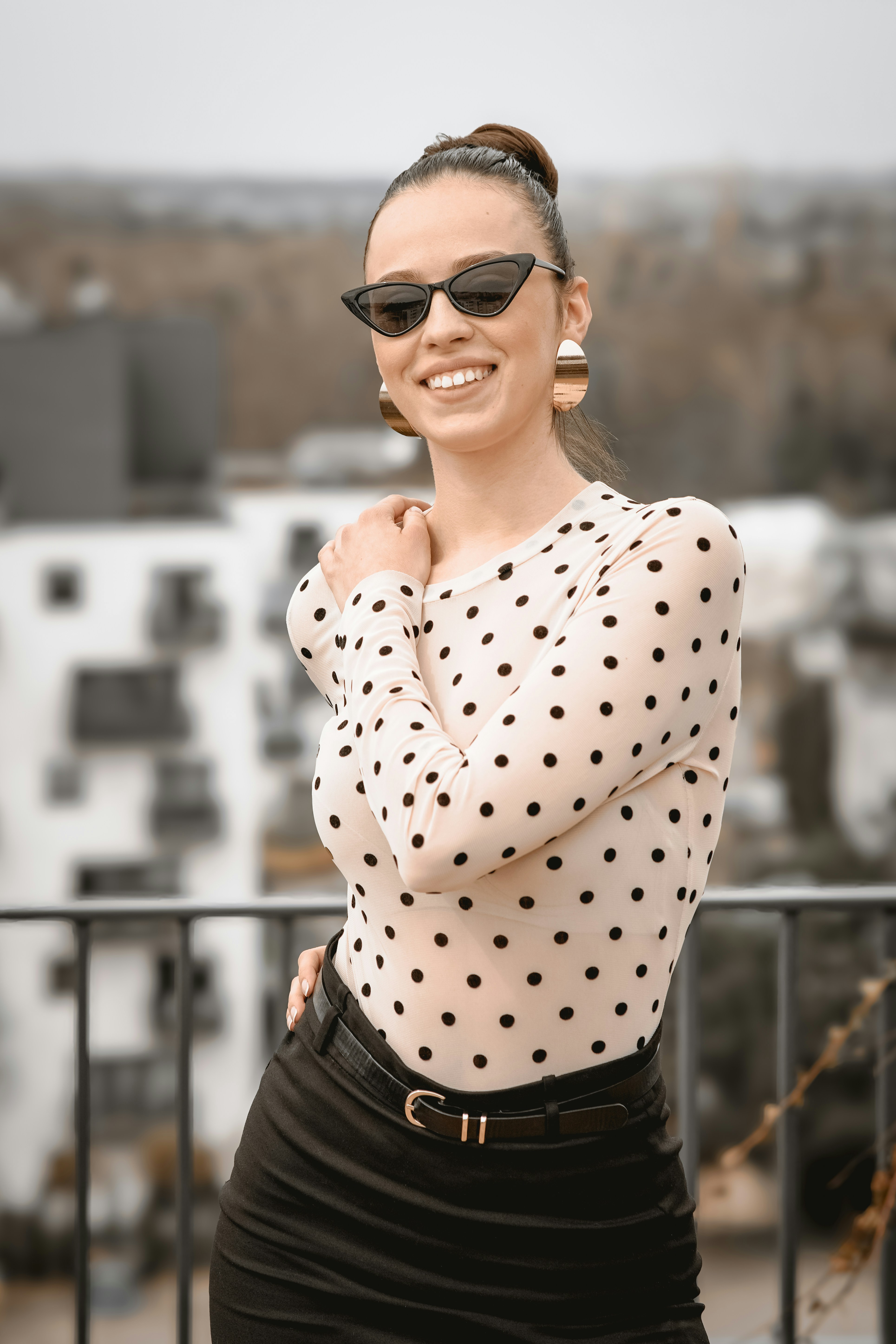 Smiling woman wearing polka dot top and sunglasses outdoors.