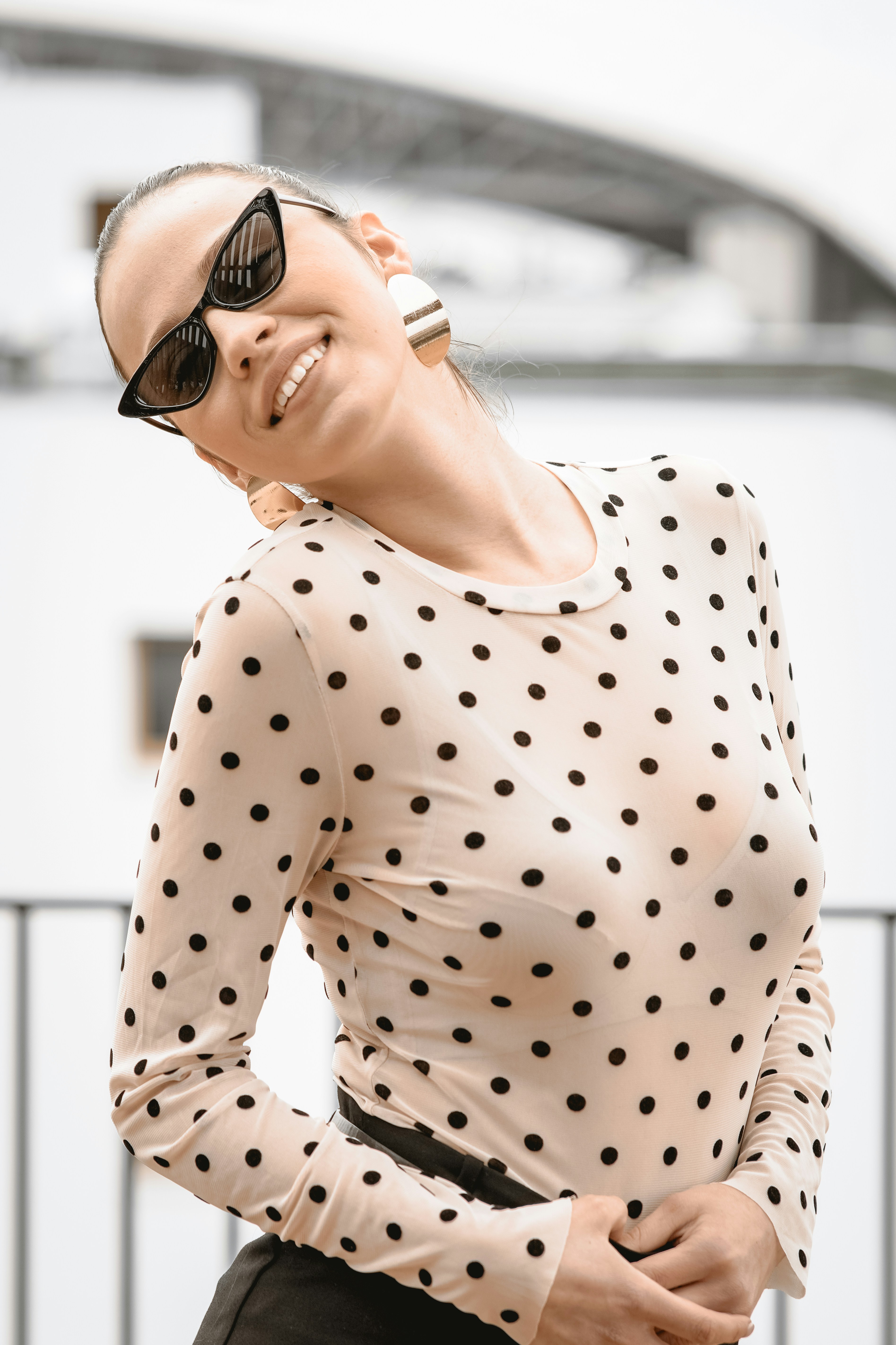 Woman smiling, wearing sunglasses and a sheer polka dot top.