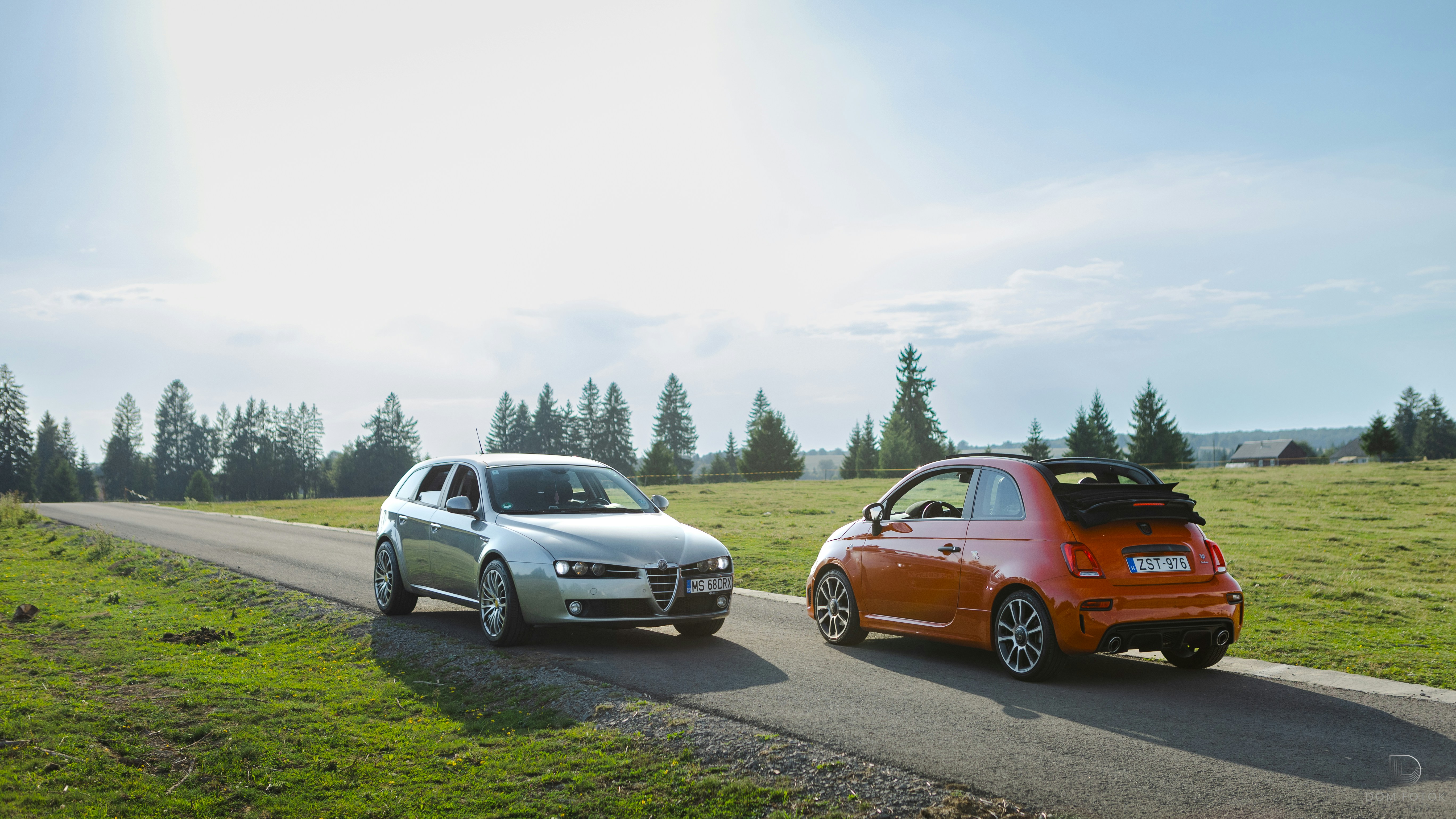 Two compact cars cruising a sunlit country road