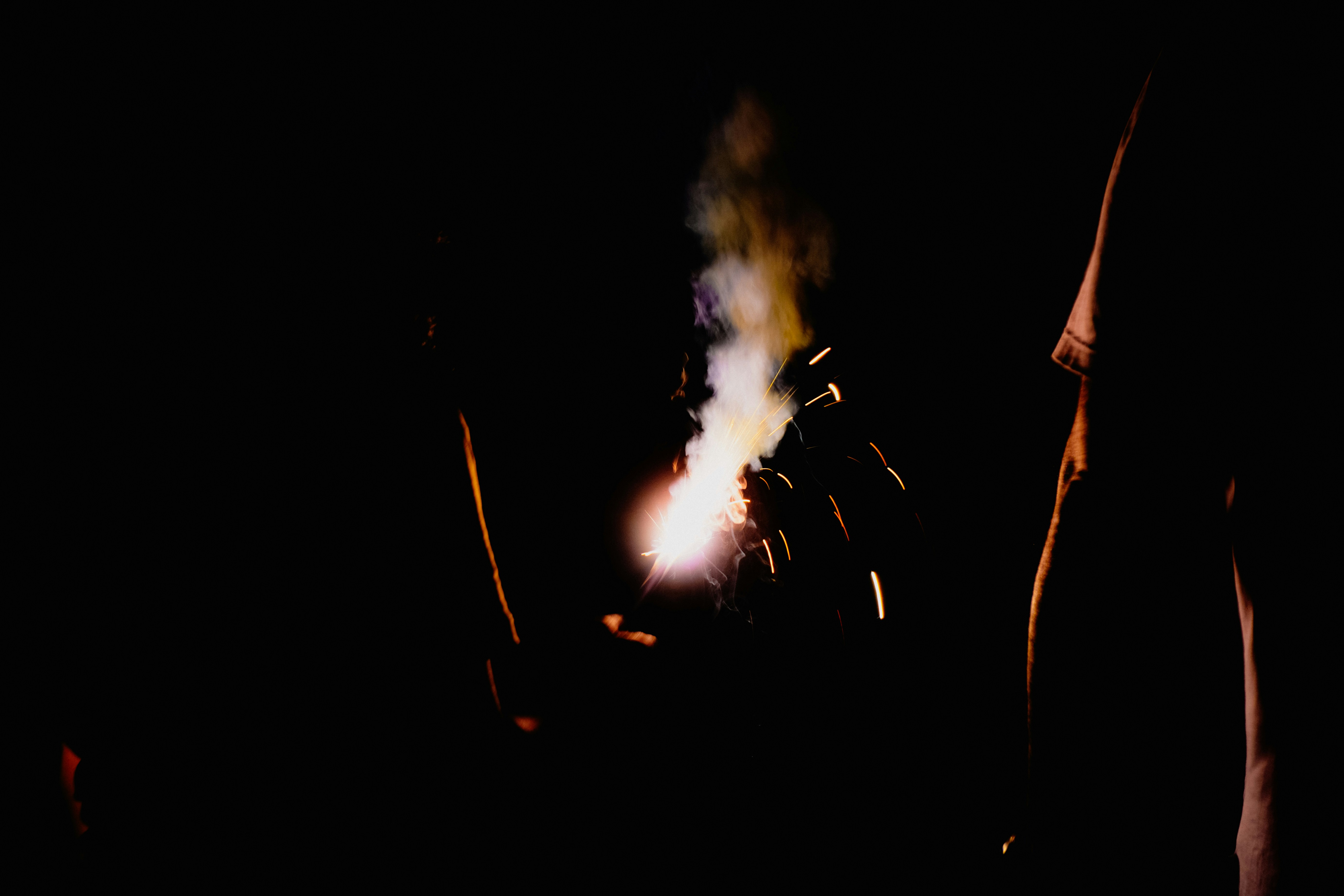 People holding a sparkler emitting light in darkness.