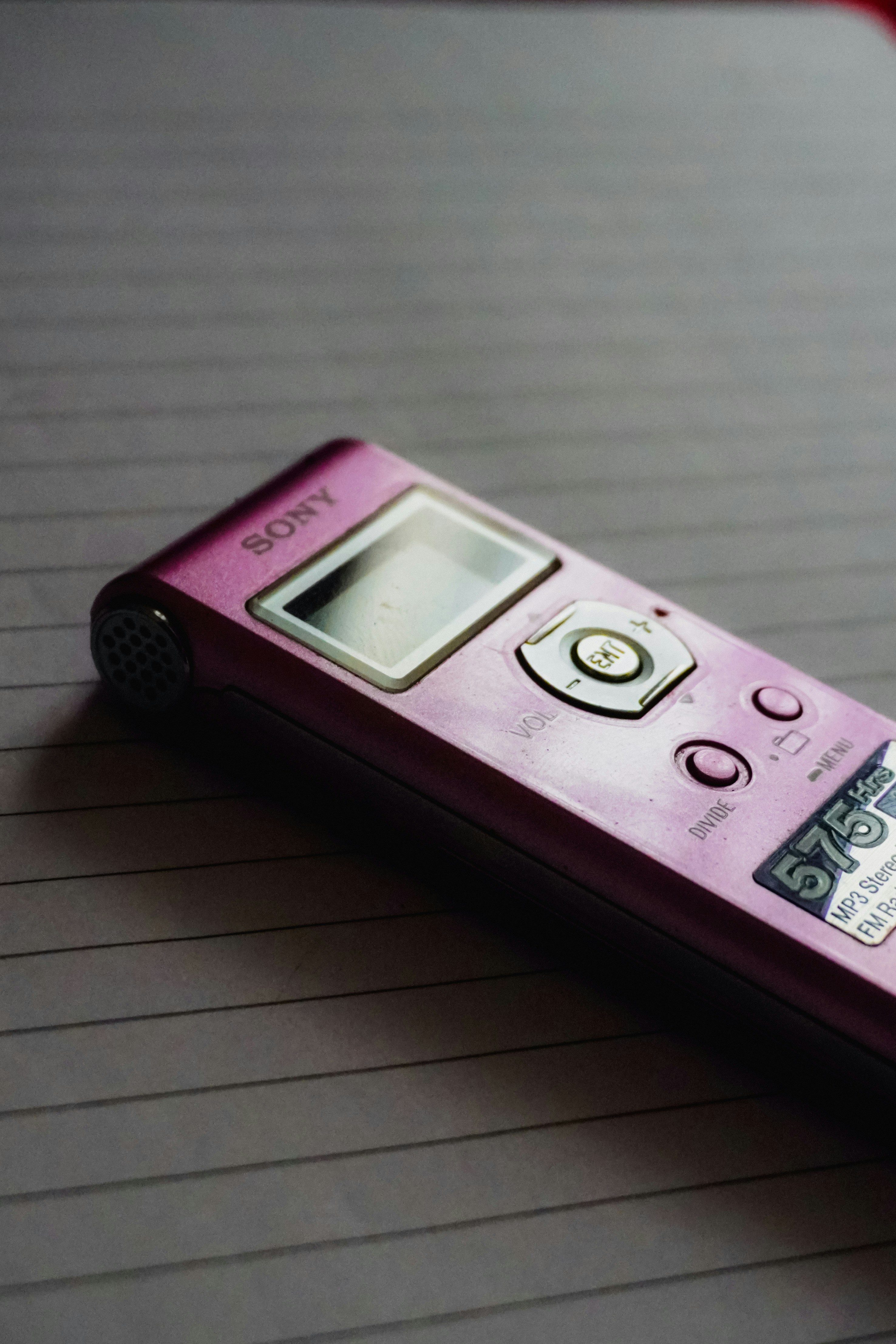 Close-up of a pink Sony handheld recorder lying on lined notebook paper, with focus on the device's buttons and display.