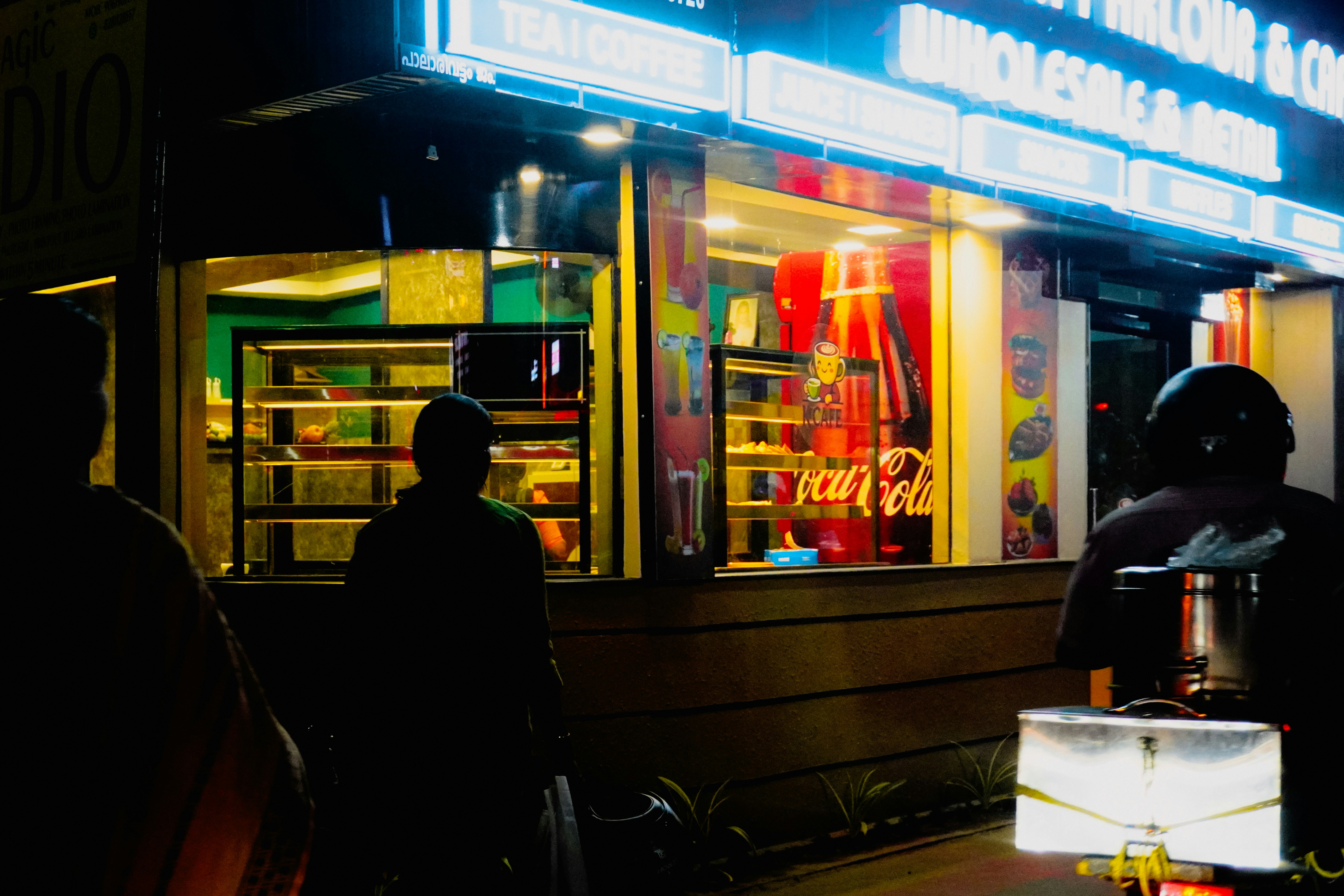 Brightly lit snack shop at night with silhouetted people.
