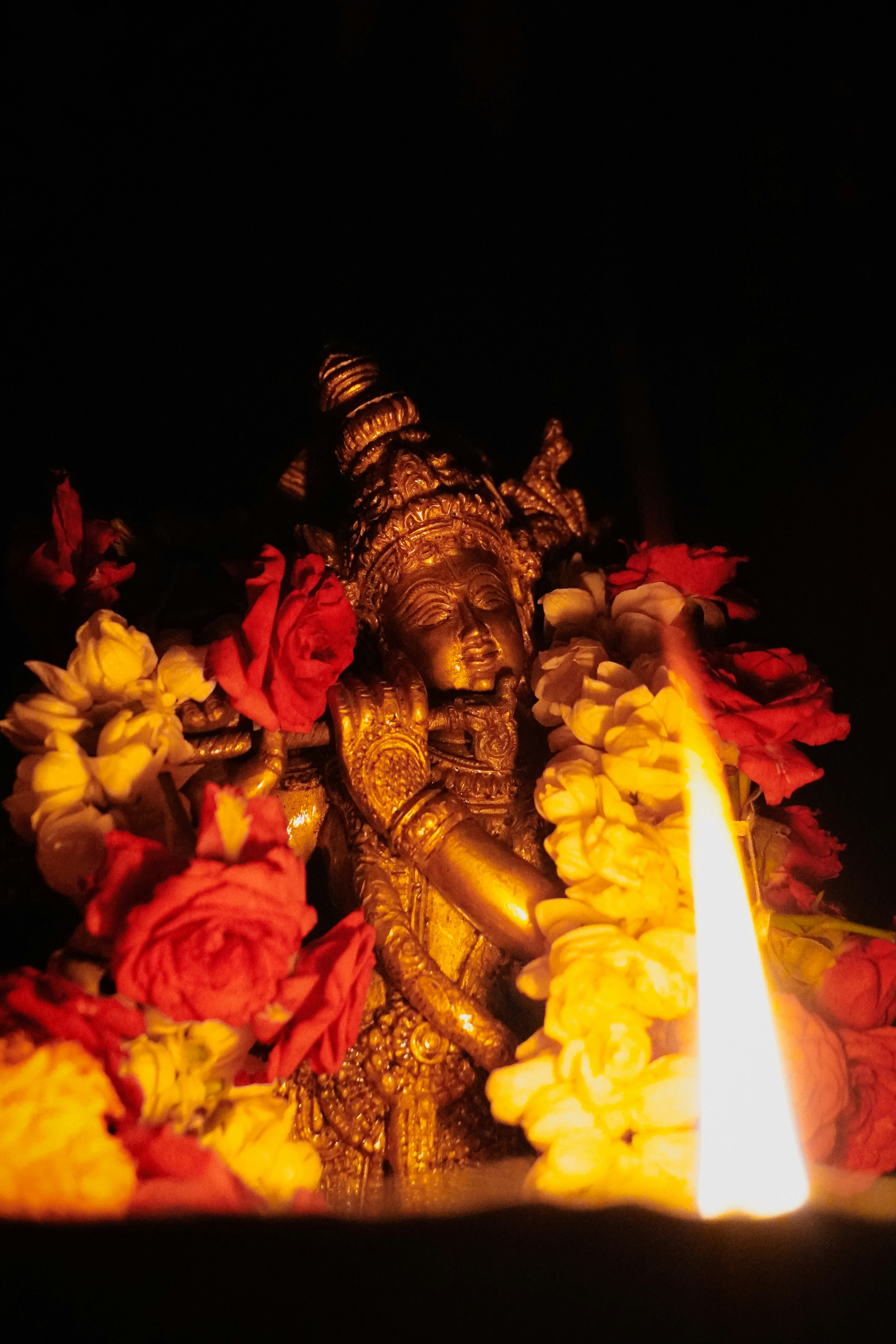 Golden deity statue adorned with flowers and a flickering flame.