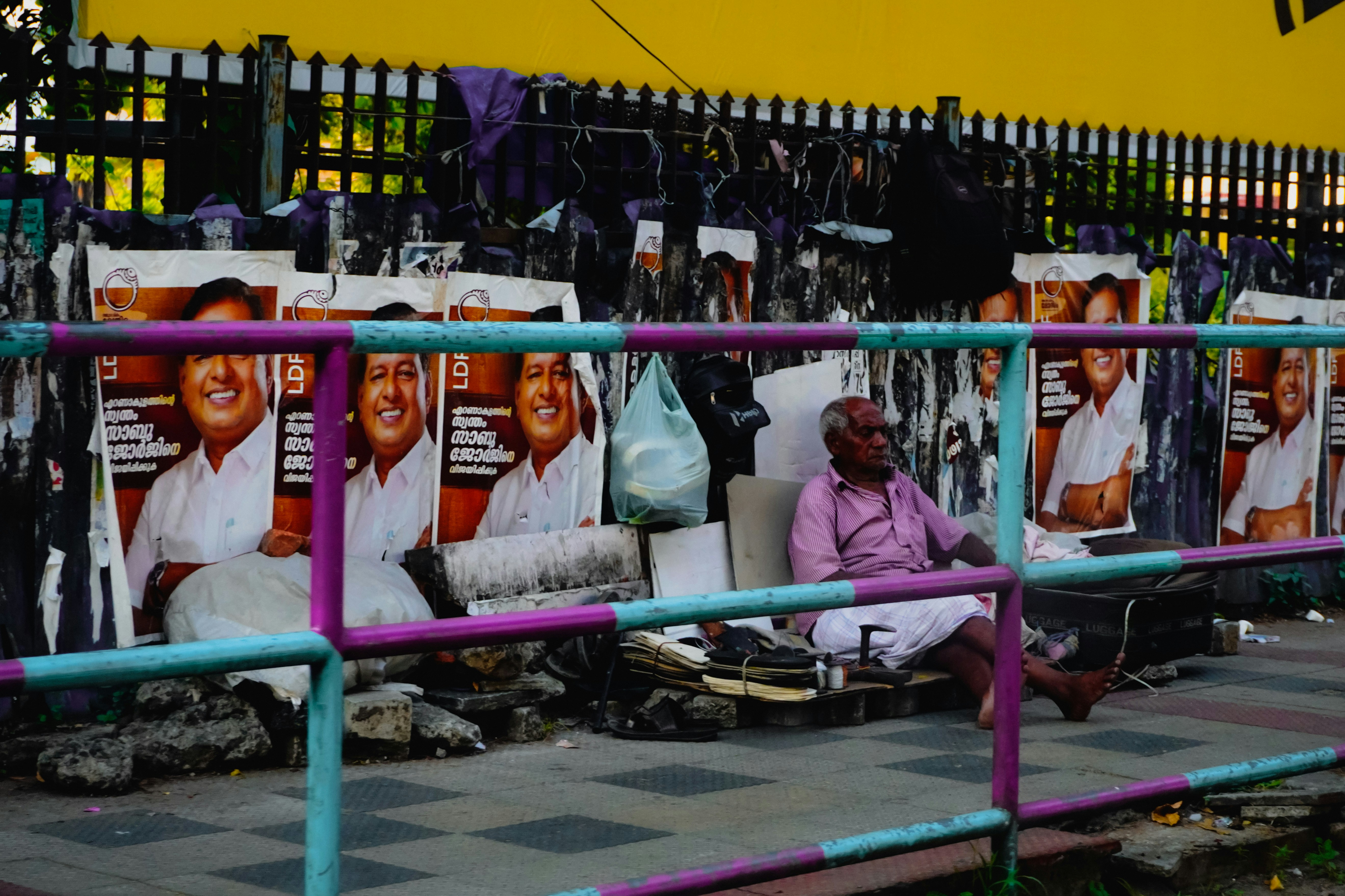 Portrait posters and a seated man beneath a colorfully barred railing