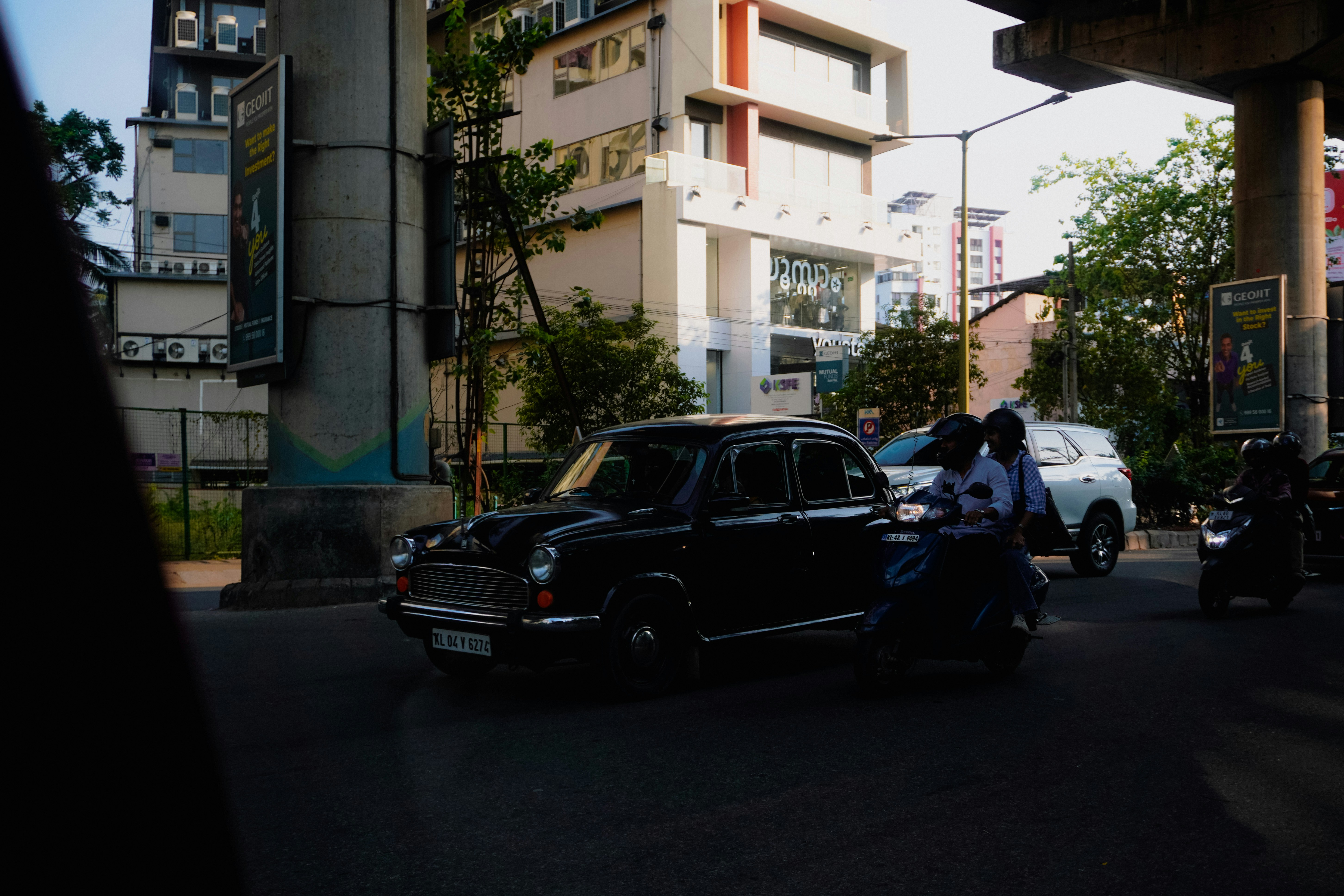 Night ride under concrete arches: a black vintage car leads a busy street scene