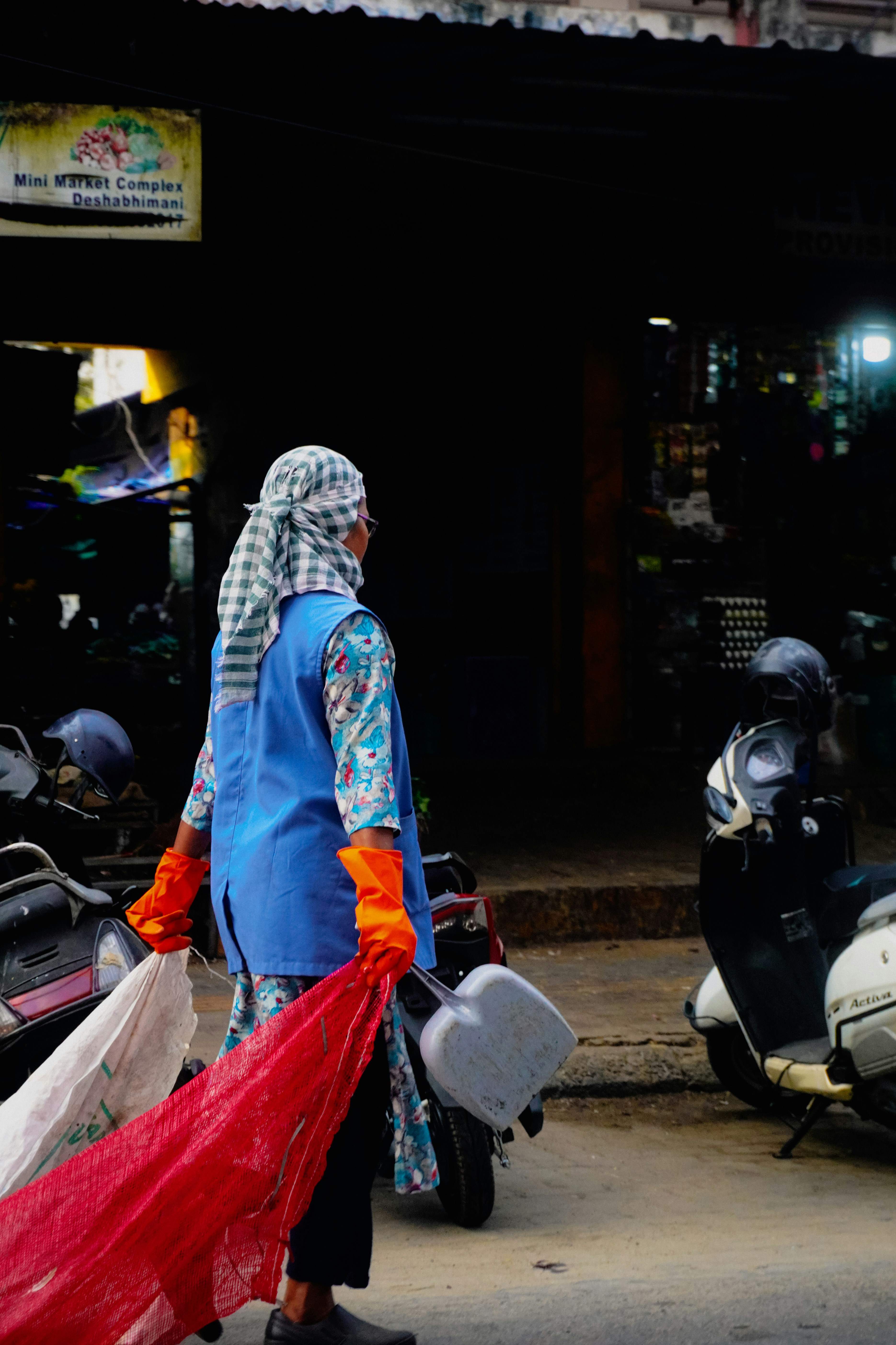 Woman carrying red fabric and container on a dark street.