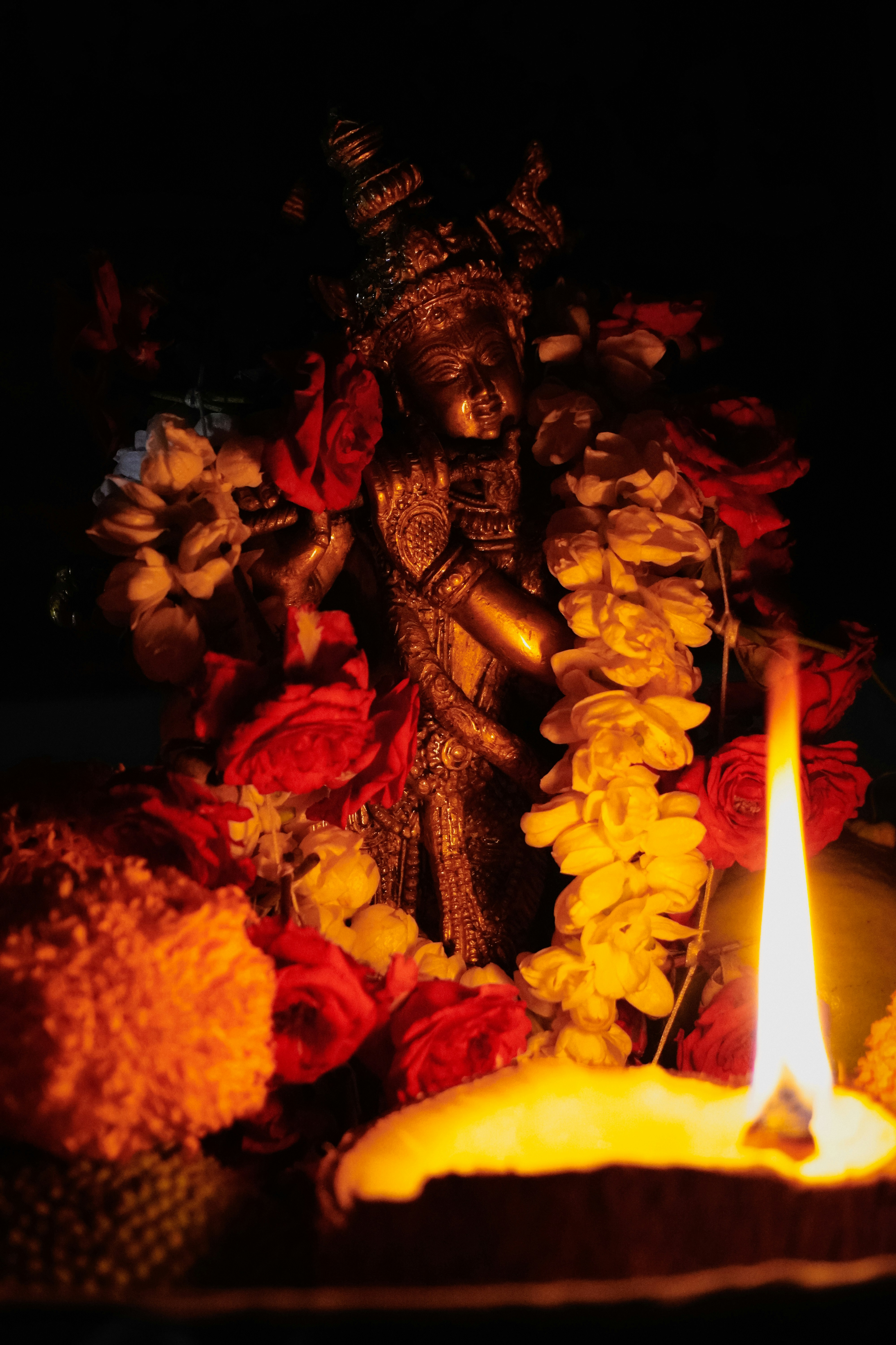 Deity statue adorned with flowers and a lit oil lamp.