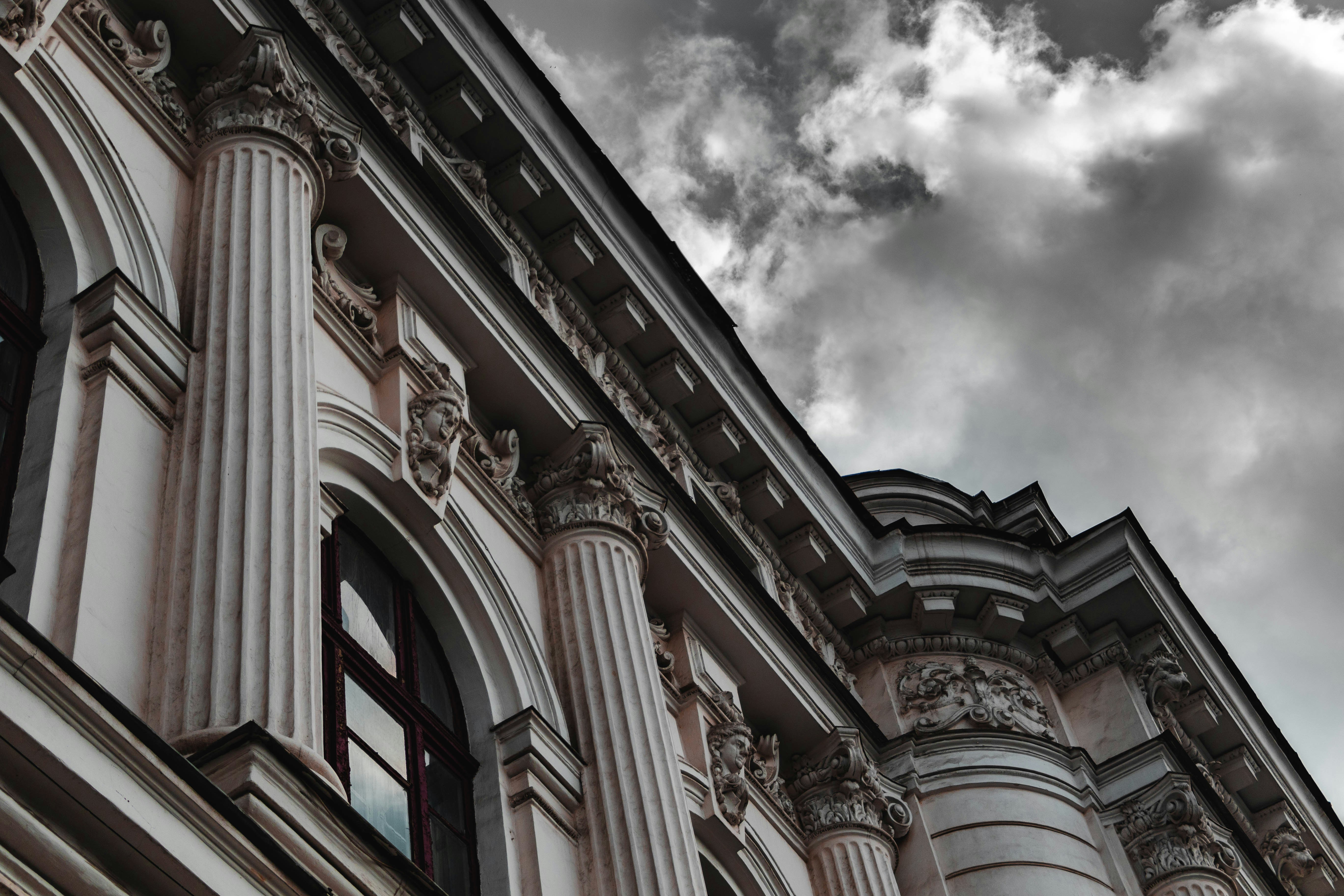 Imposing neoclassical building details with fluted columns and ornate capitals beneath a dramatic cloudy sky.