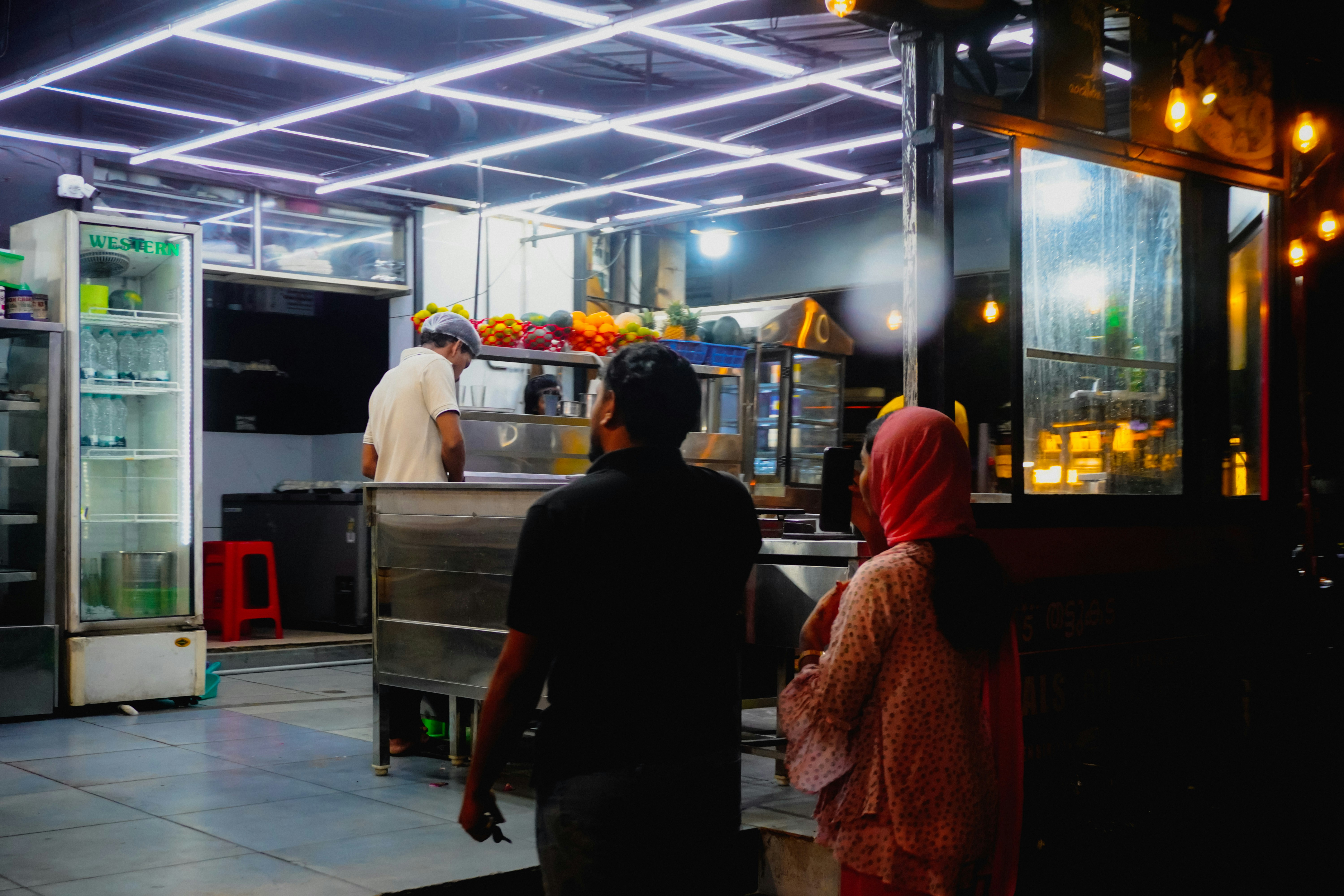 People standing at a brightly lit food stall at night.