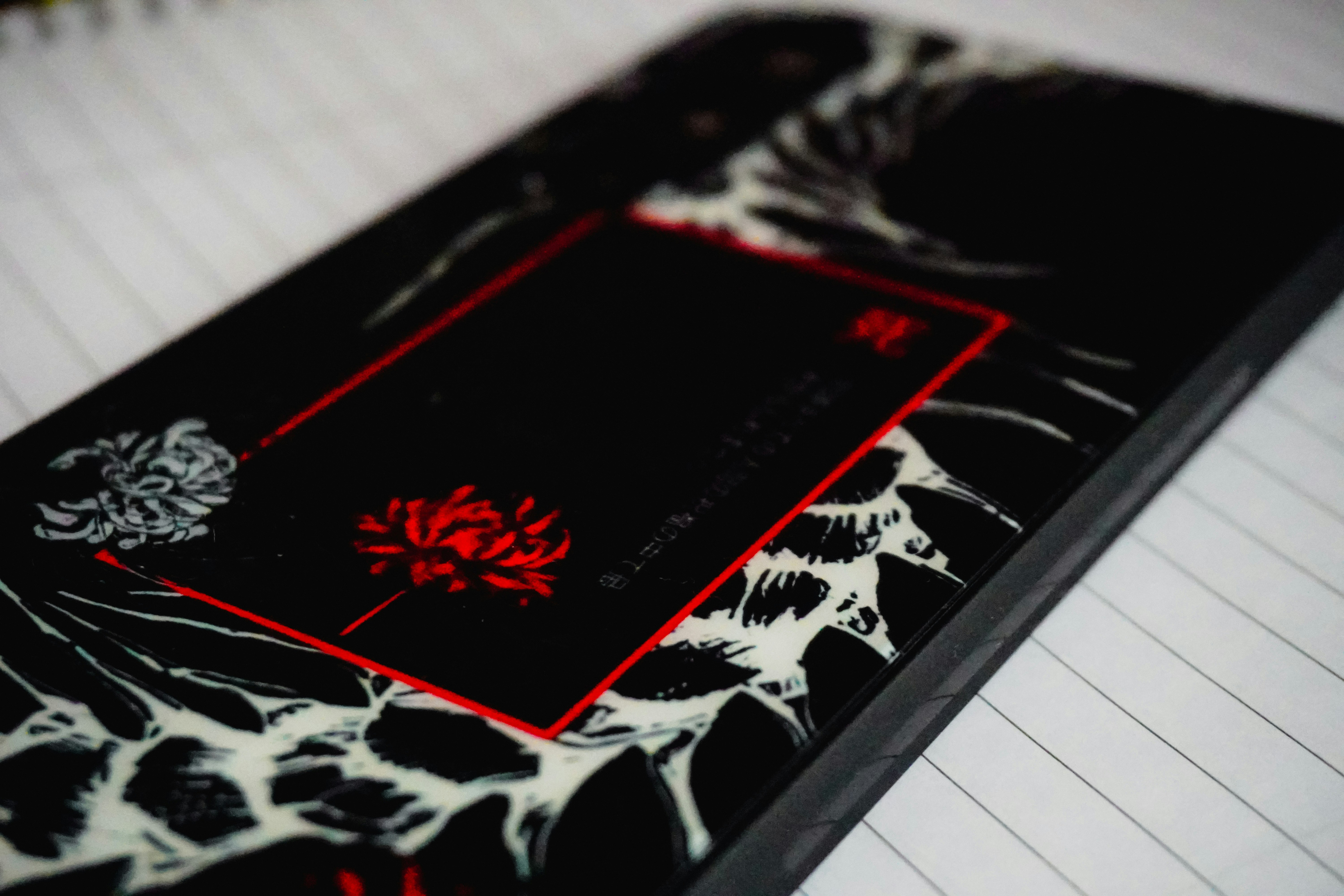 Close-up of a black notebook with red floral embossing resting on lined paper; a bold red frame highlights the center motif, suggesting a decorative or branded cover.