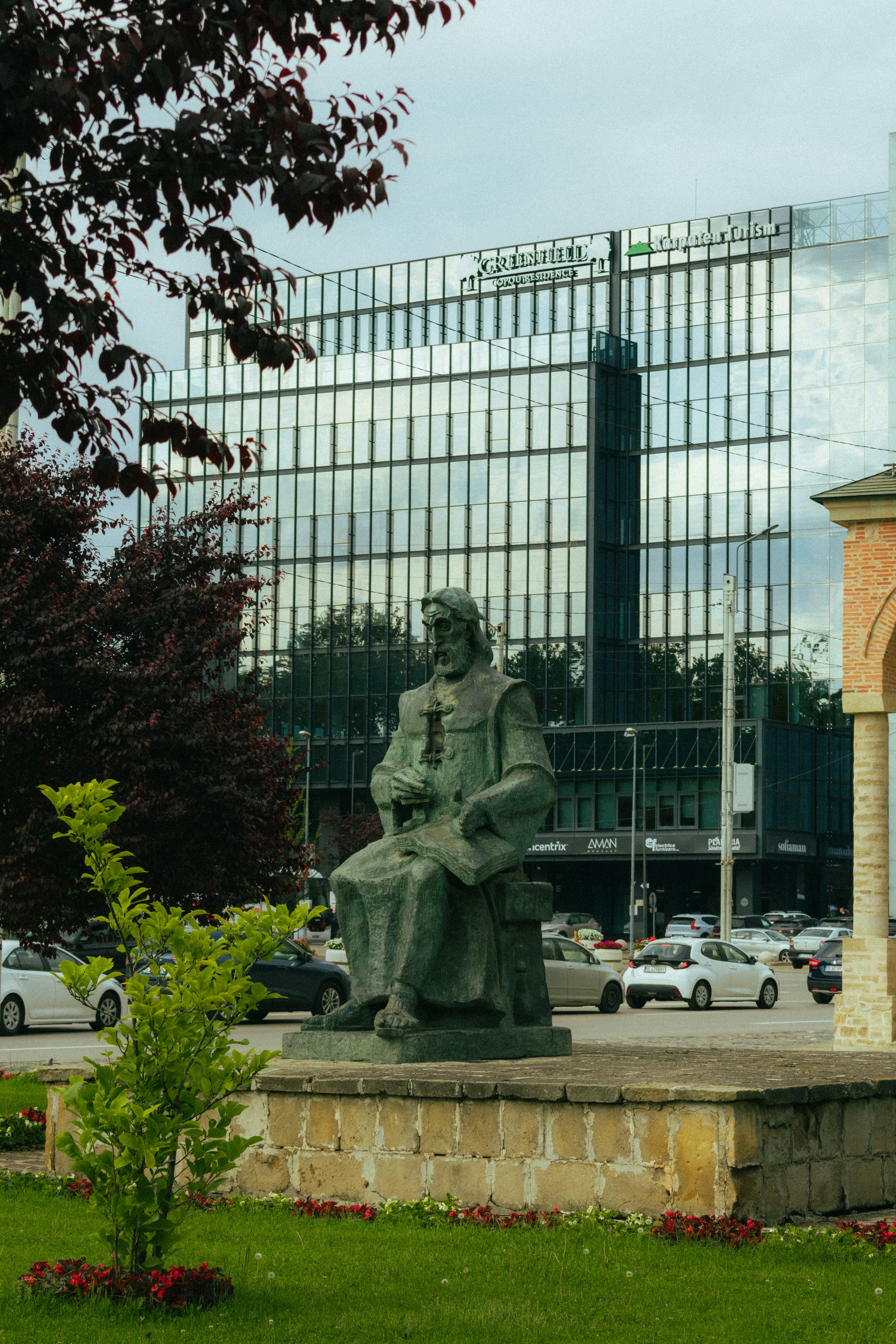 Bronze scholar: a seated statue framed by a modern glass facade